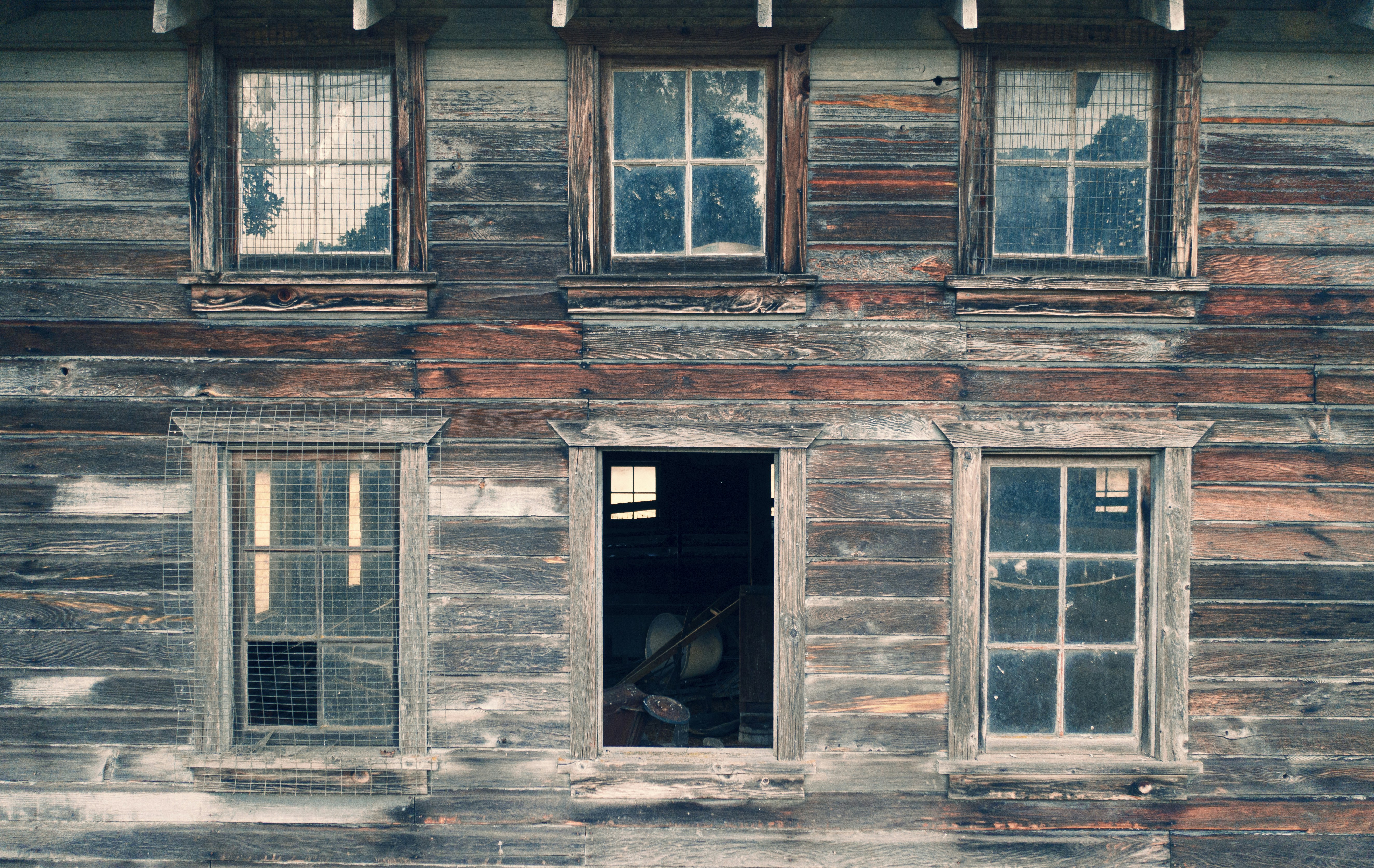 Weathered wooden building facade with multiple windows, one open to reveal interior clutter.