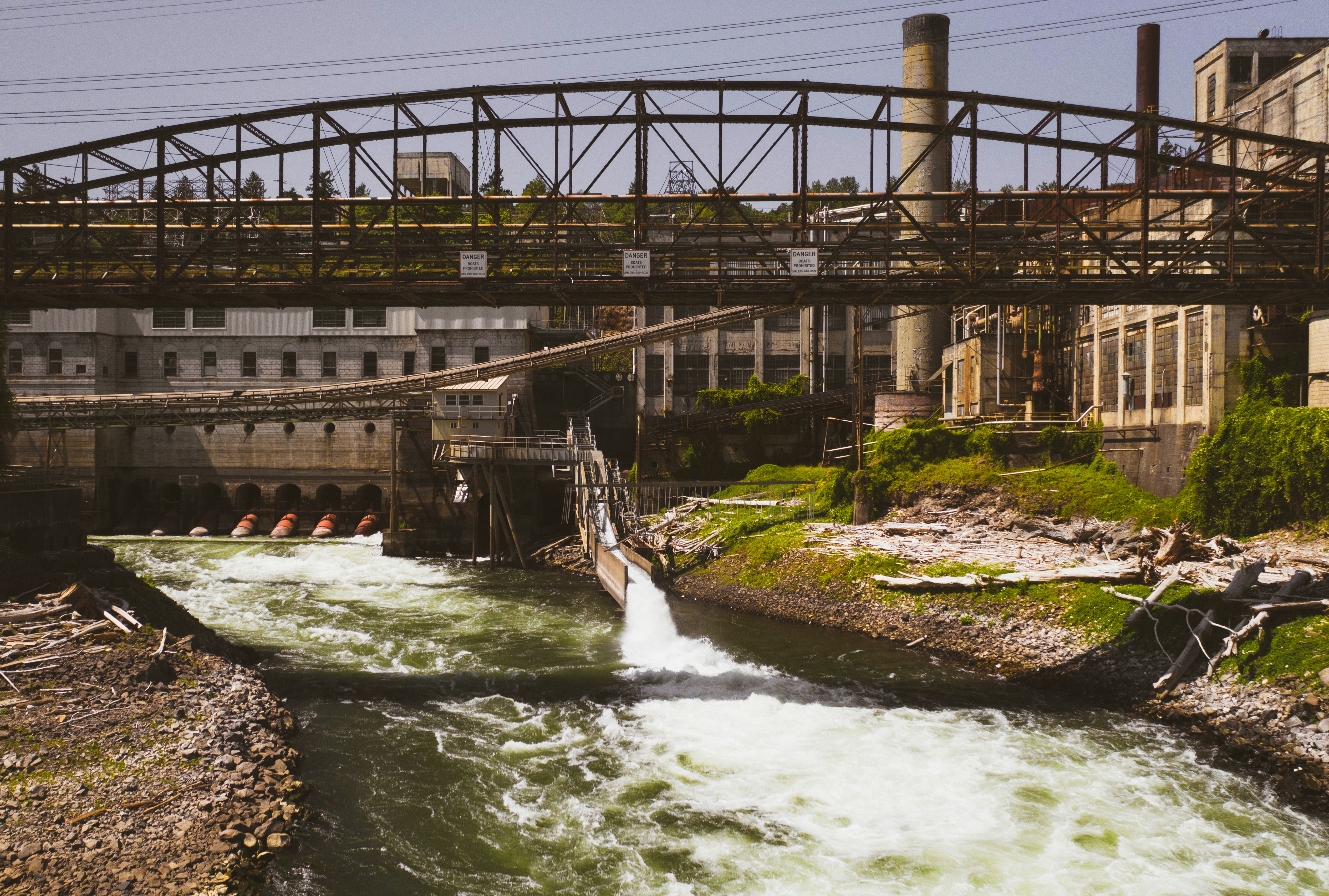 Historic hydroelectric plant on the Willamette River with a steel bridge and flowing water.
