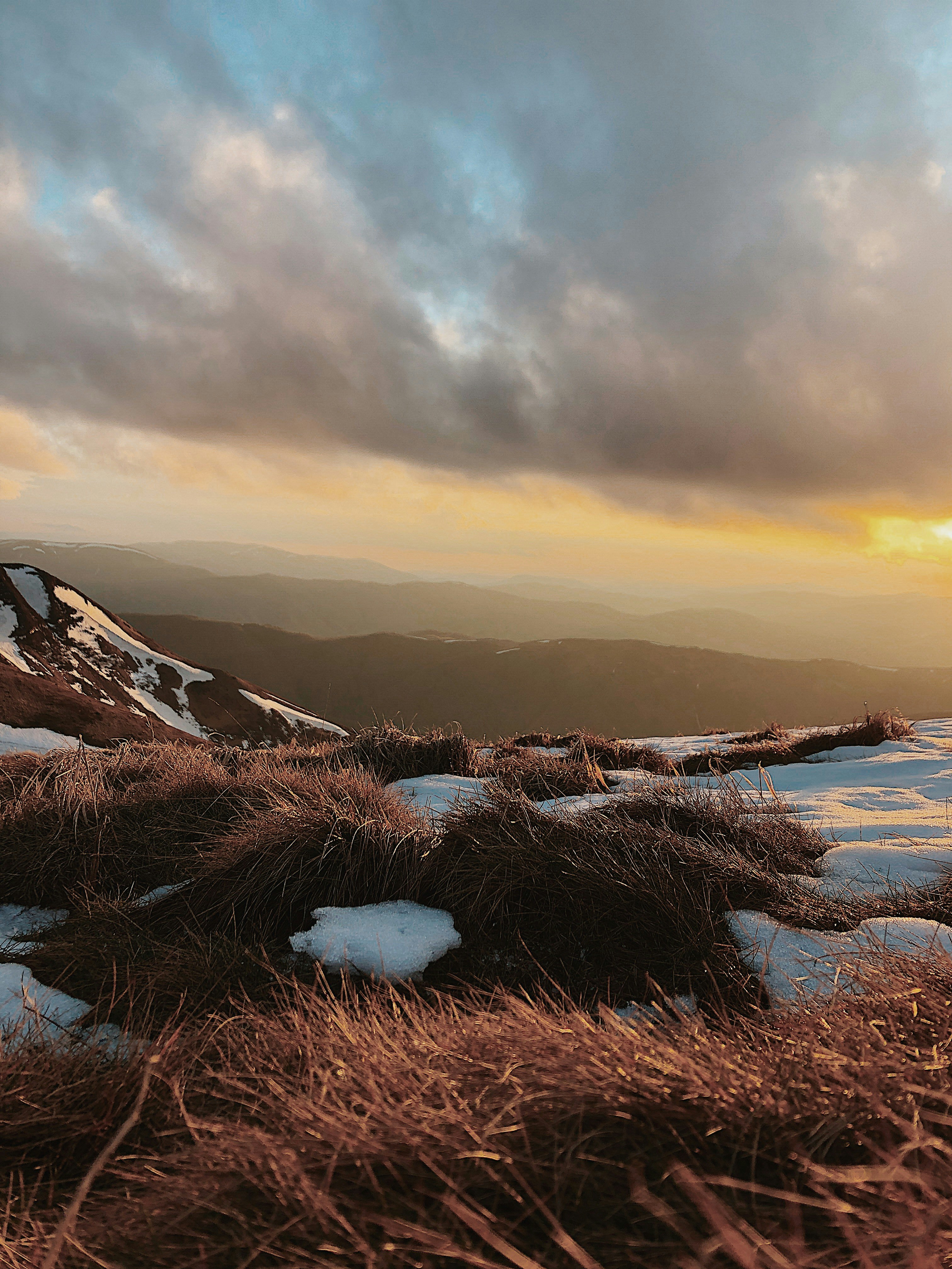 Golden sunset illuminating the snow-capped mountains and grassy foreground, showcasing the transition from winter to spring.