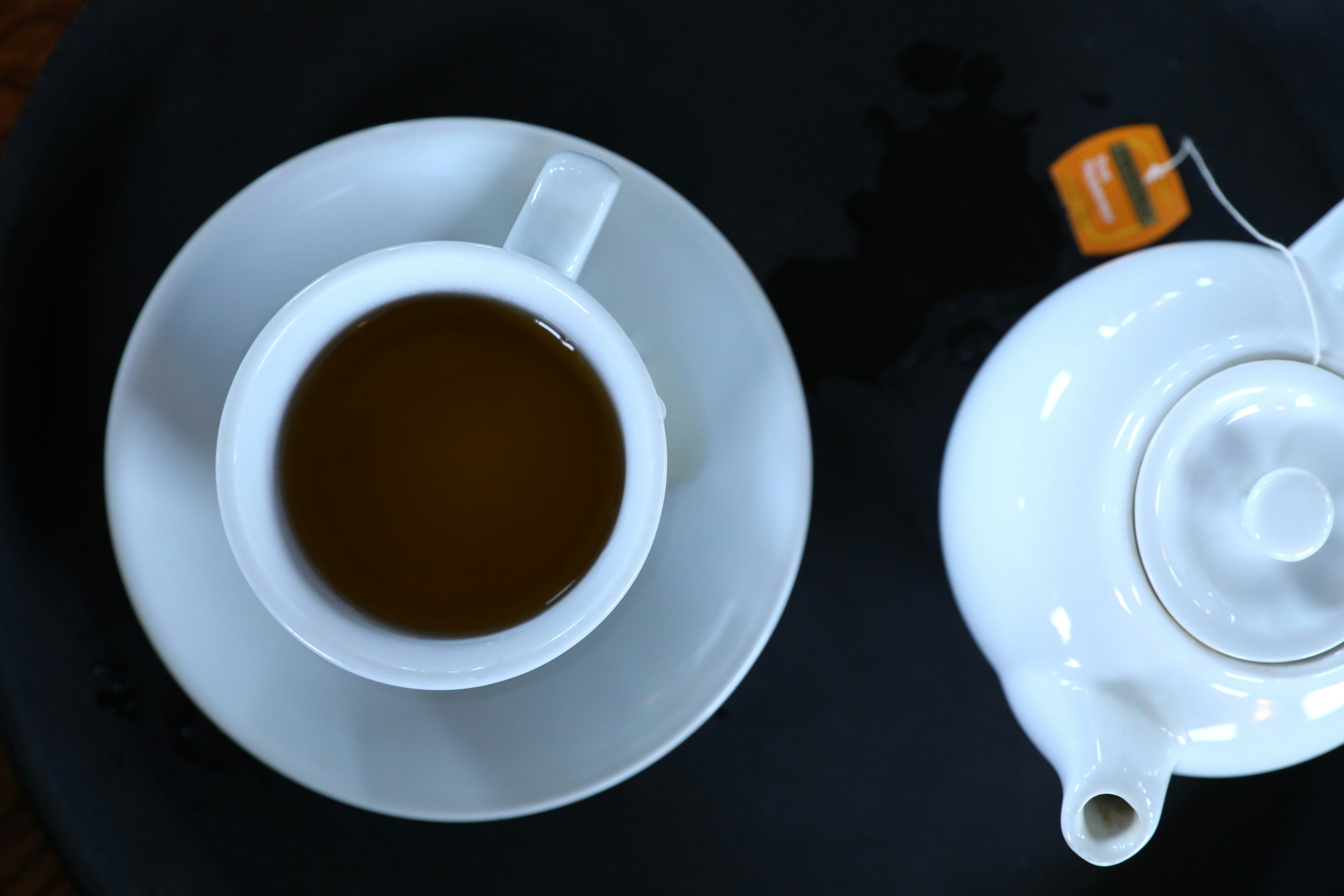 A top-down view of a white teacup filled with tea alongside a teapot, resting on a dark tray. The simplicity highlights the elegance of the tea ceremony.