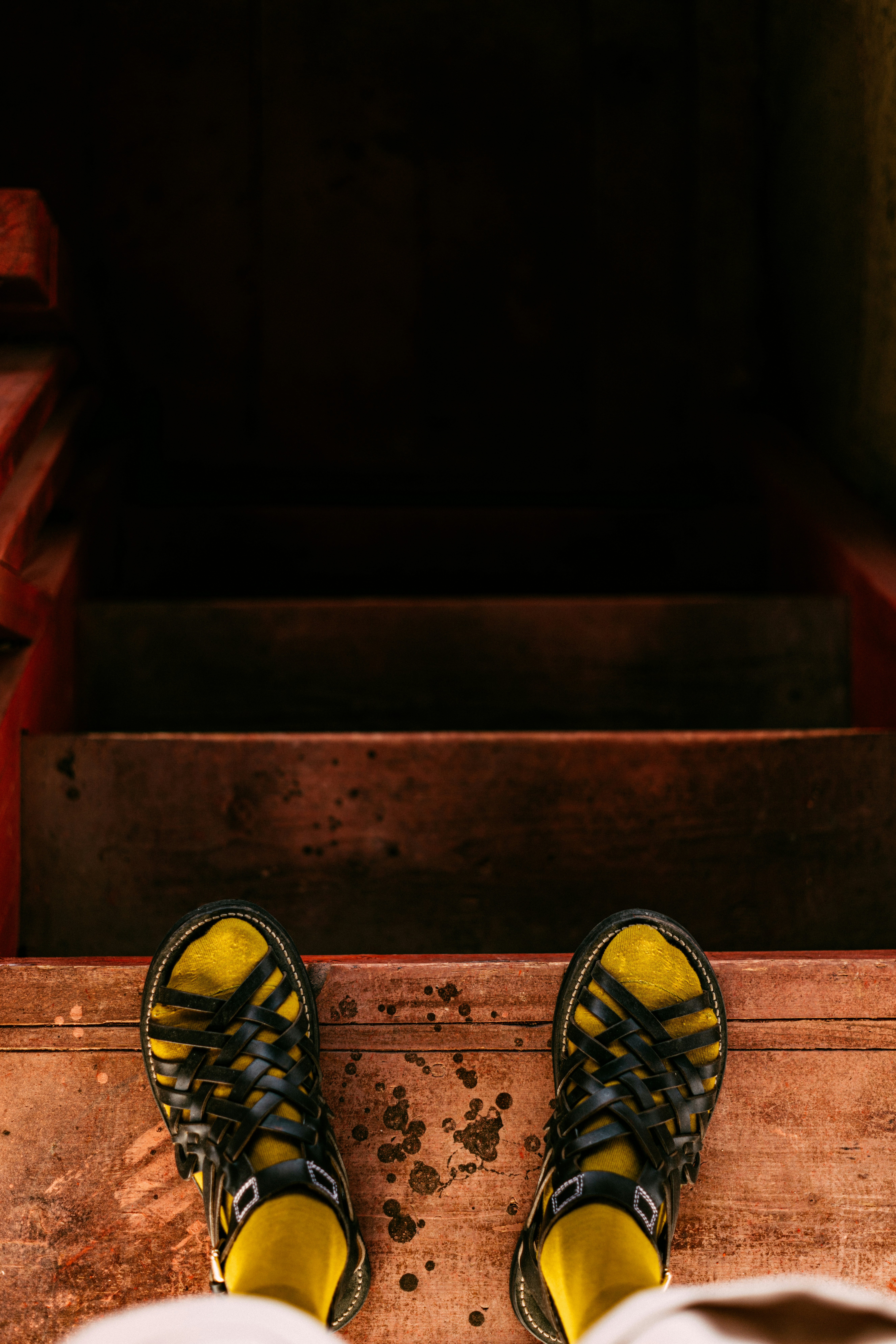 Feet clad in black sandals and bright yellow socks poised on weathered wooden stairs leading downward.