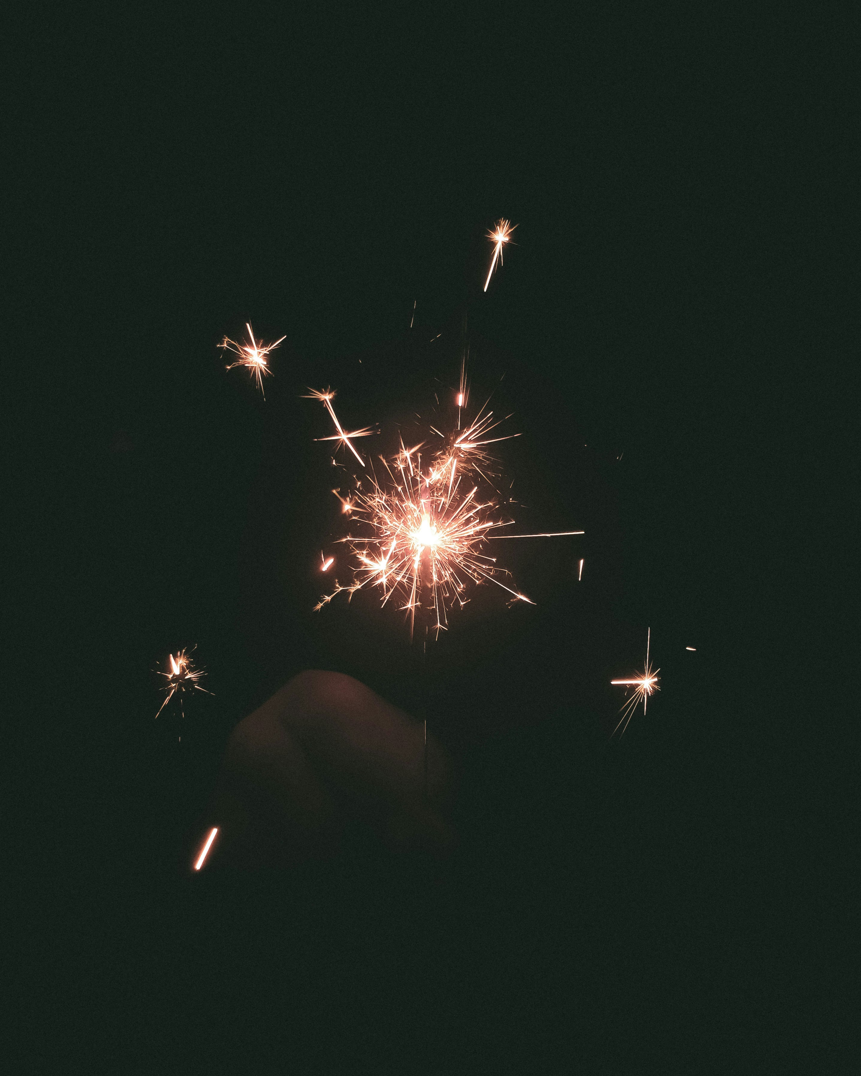 A hand holding a sparkler, emitting bright sparks against a dark background, creating a mesmerizing display of light.