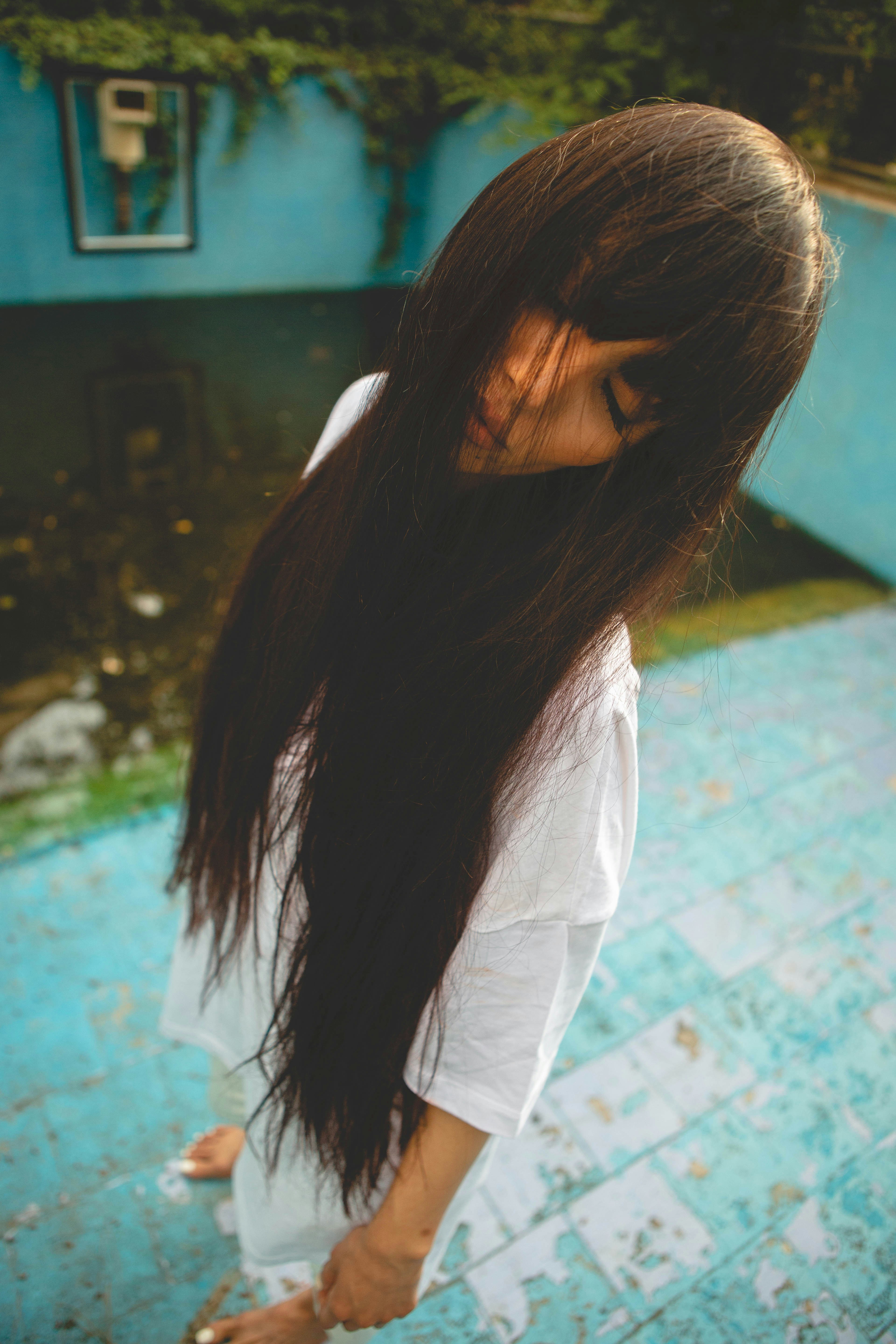 A young woman with long hair stands pensively over a turquoise surface, surrounded by reflections of nature. The atmosphere evokes a sense of calm and introspection.