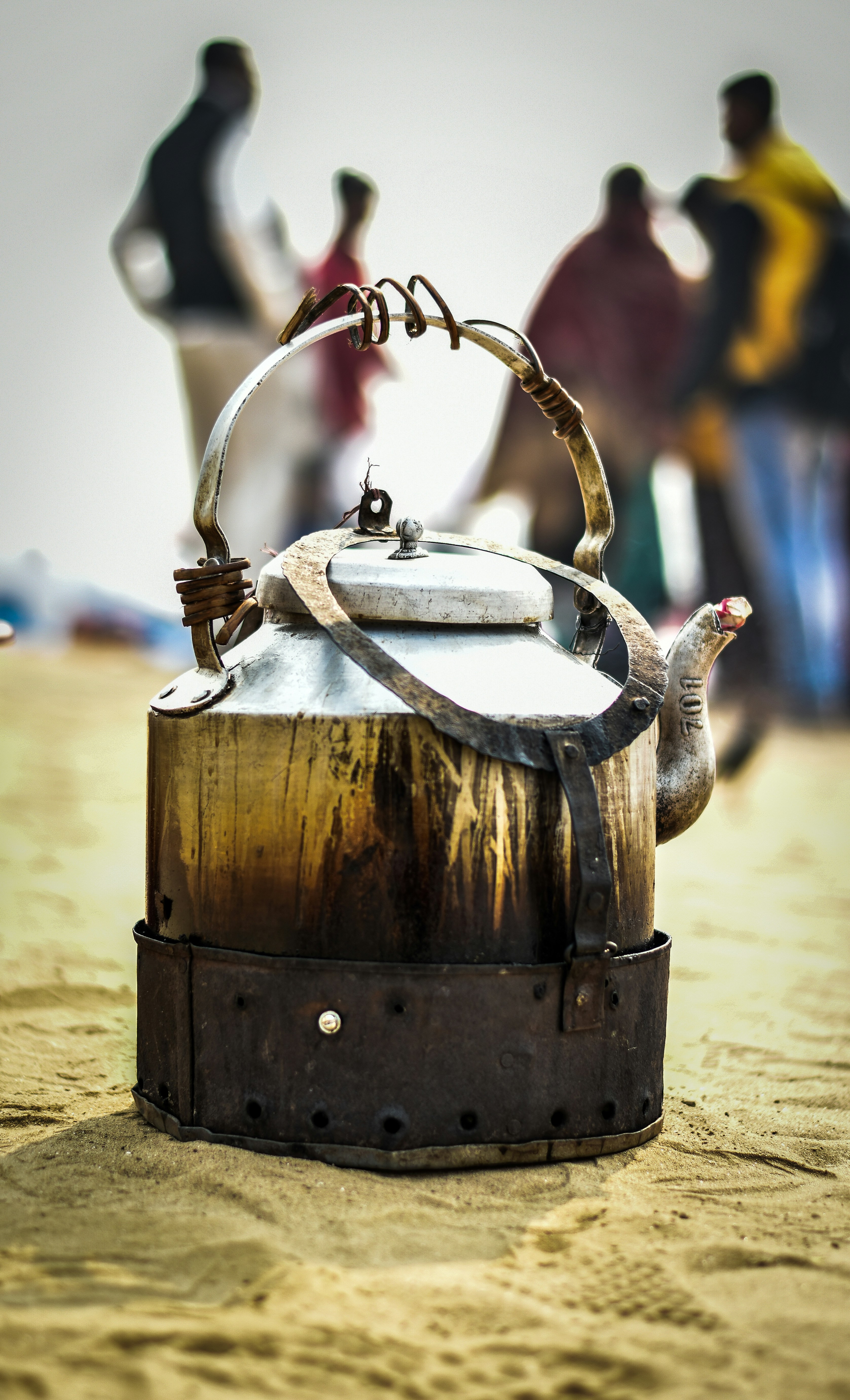 Kettle on Sand: a Weathered Sentinel Amid Blur of Beachgoers