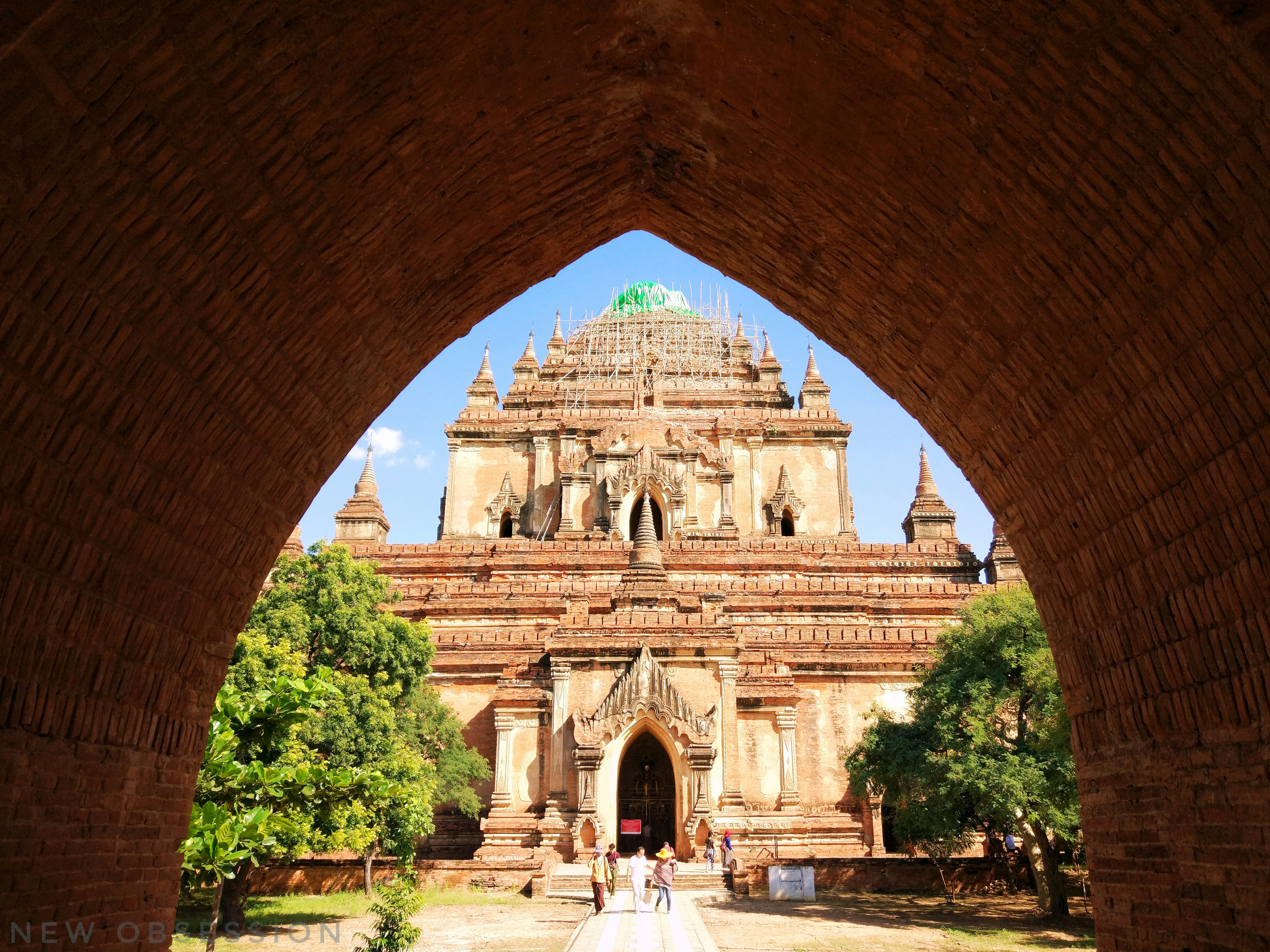 Historic temple complex framed by an arched entrance, showcasing intricate architecture against a clear blue sky.