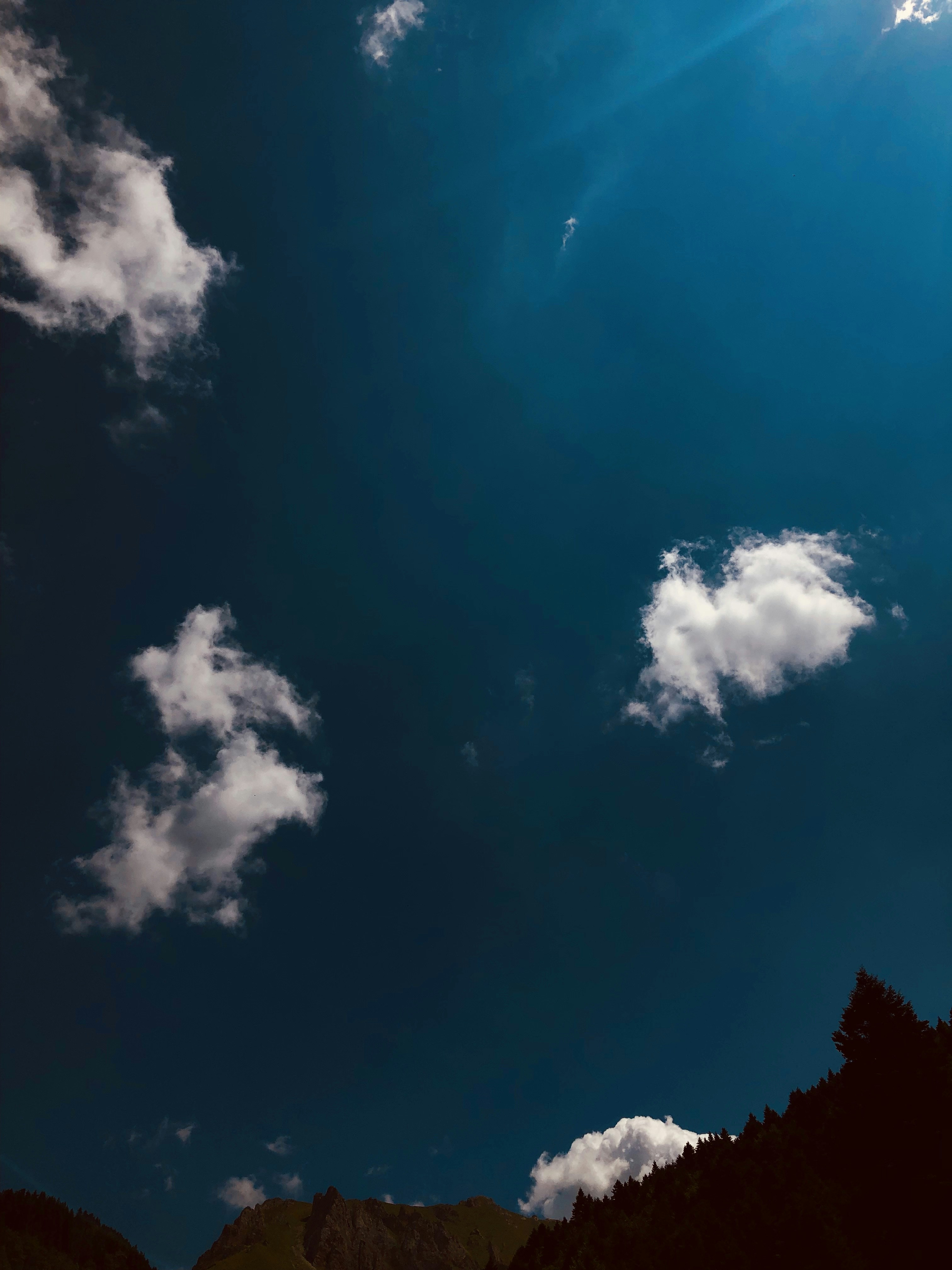 Vast blue sky adorned with fluffy white clouds, framed by distant mountain silhouettes. A serene atmosphere envelops the scene.