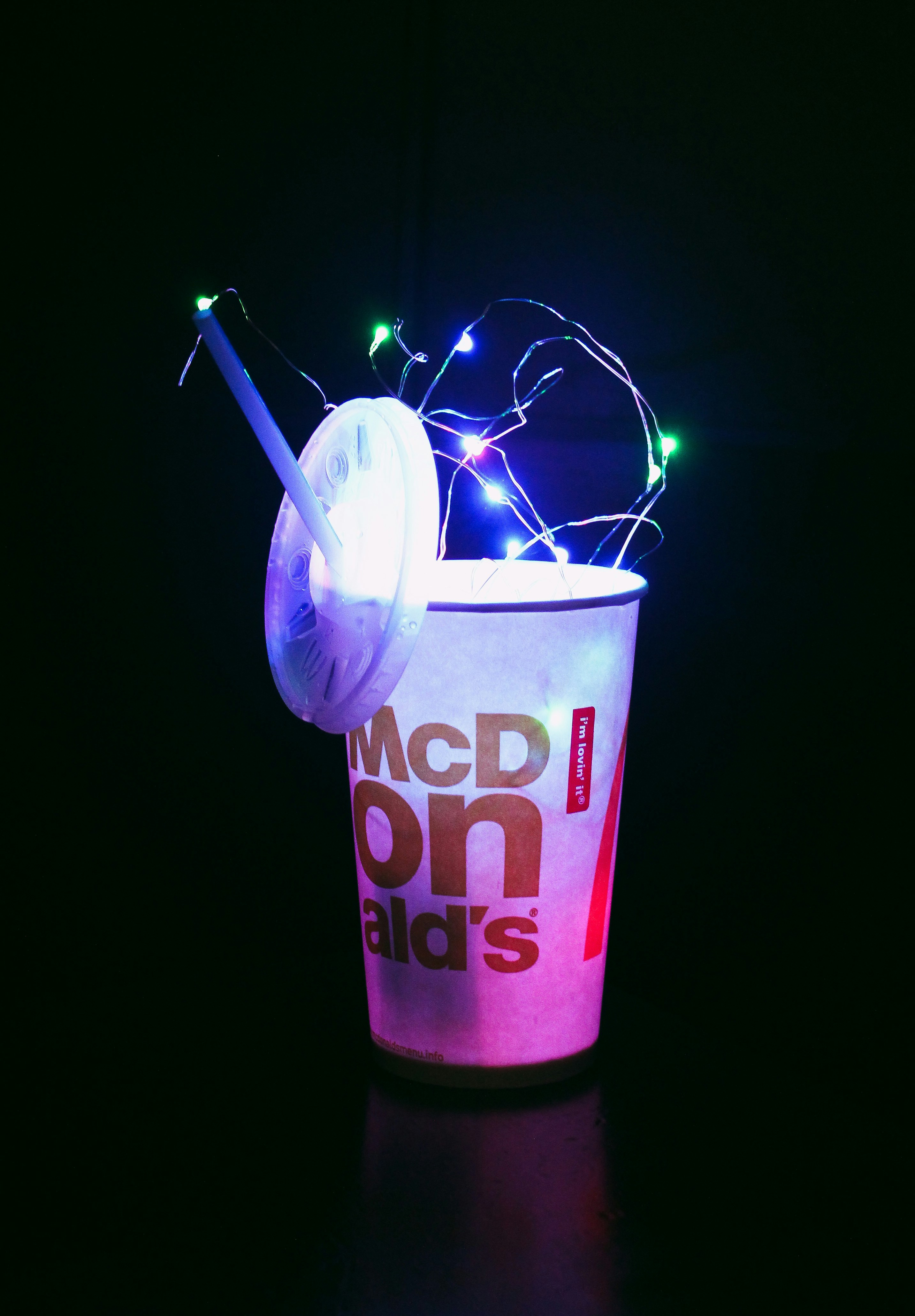 A McDonald's cup with a straw, adorned with colorful LED lights, set against a dark background, creating a whimsical and vibrant effect.