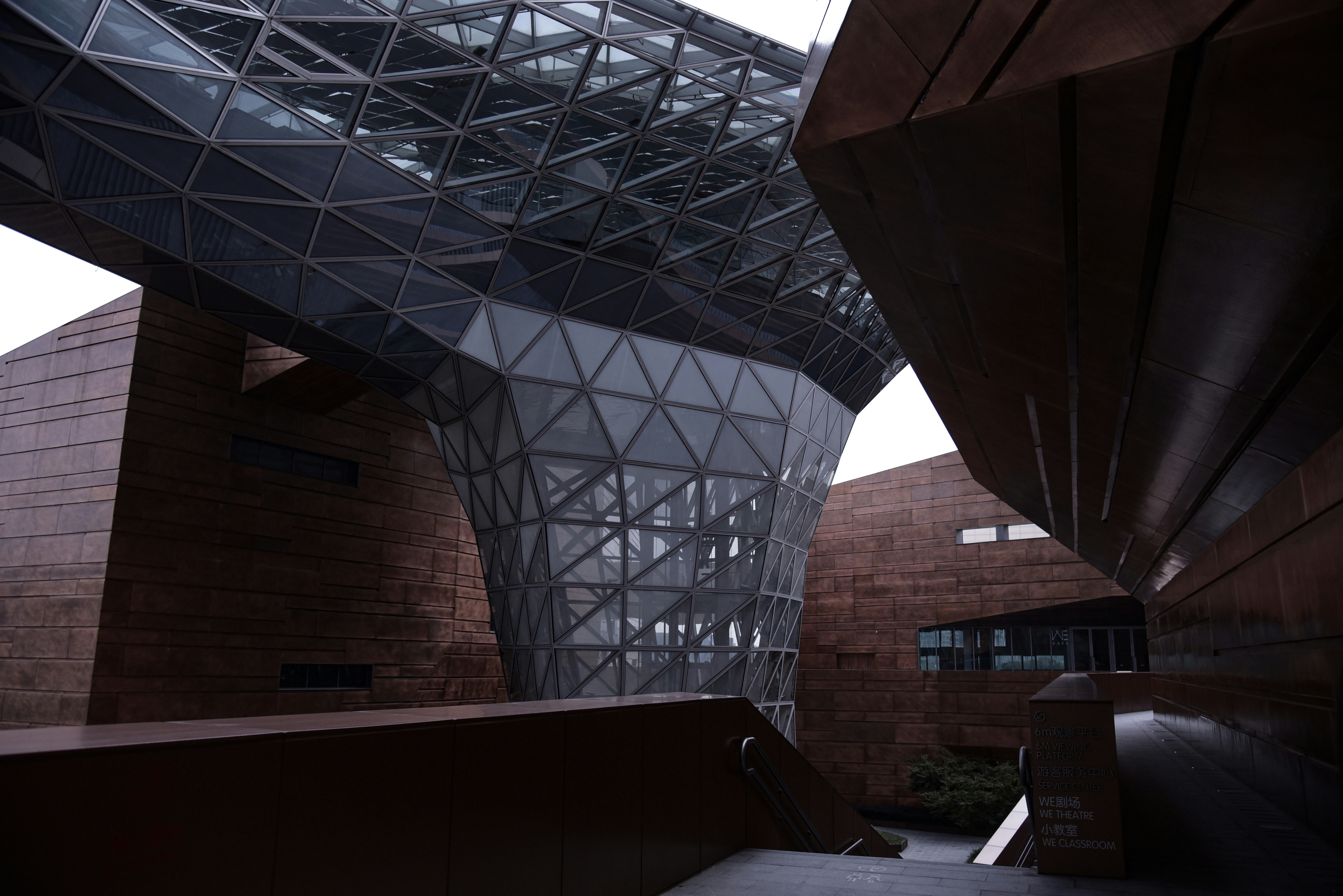 Intricate architectural design featuring a geometric glass structure intertwined with angular metallic elements. The composition highlights the contrast between light and shadow.