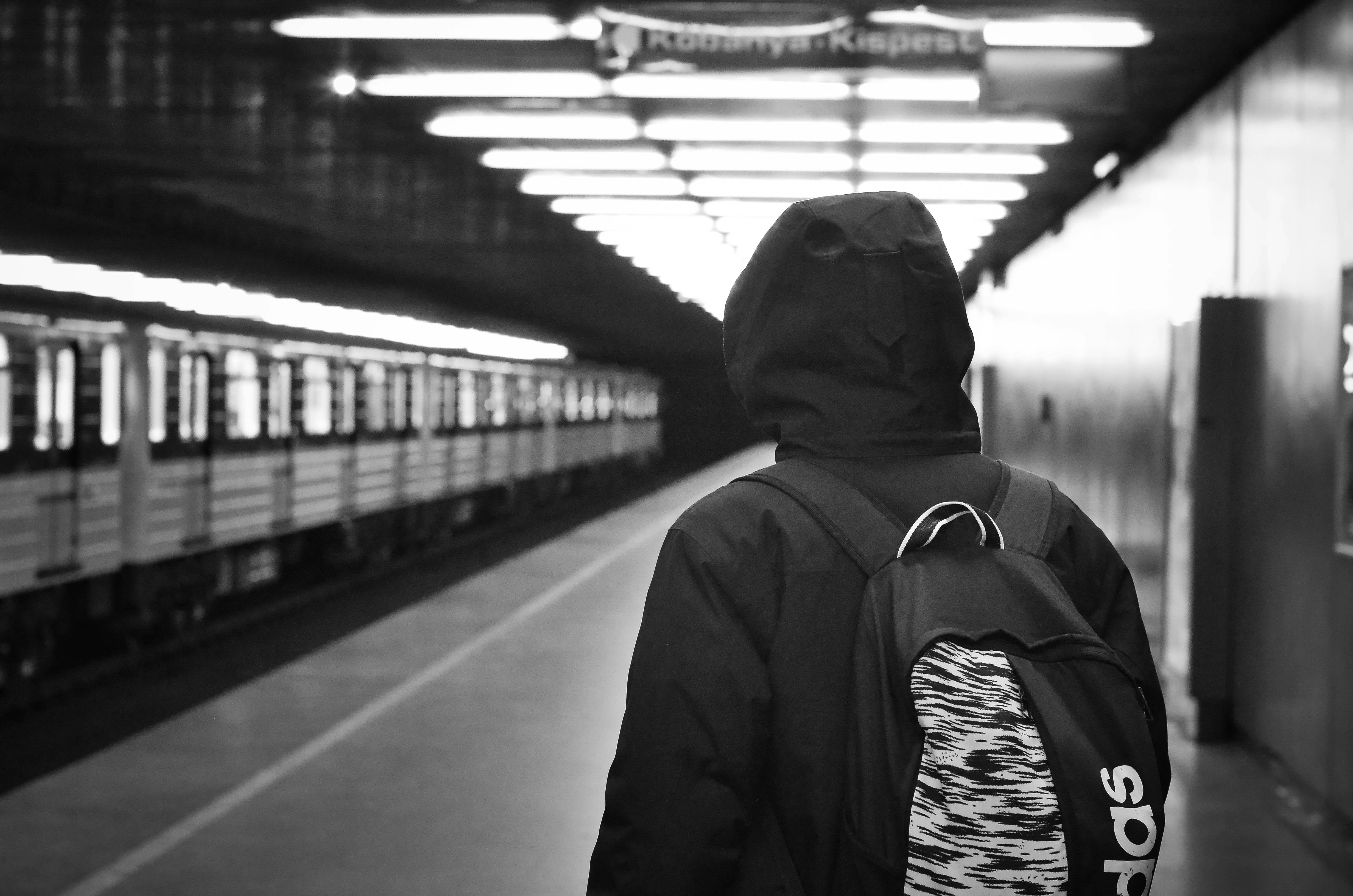 Monochrome Quiet: Hooded Traveler with Striped Backpack on a Subway Platform