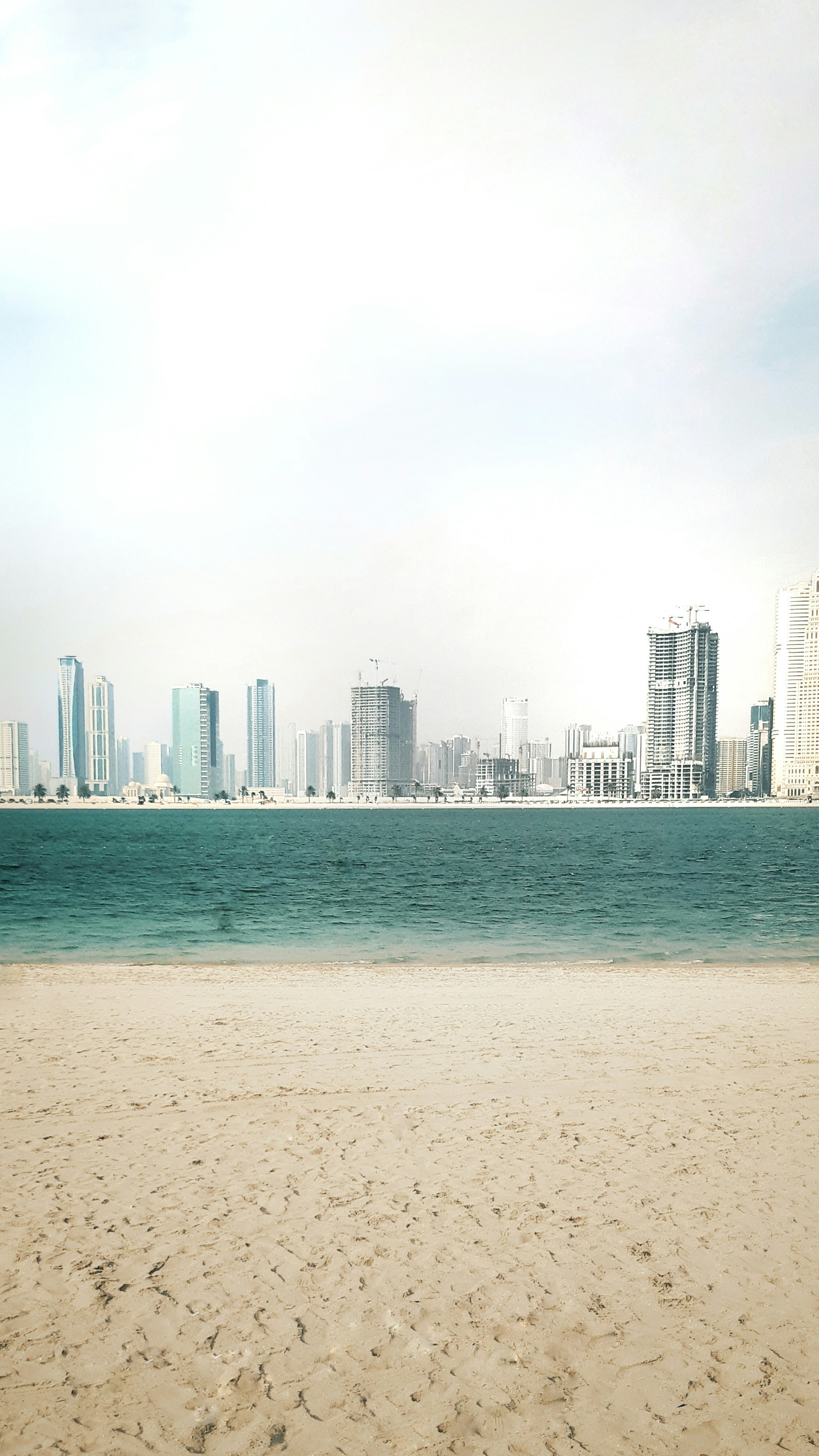 Sunlit beach with smooth sand and turquoise water stretches toward a distant skyline along the horizon.