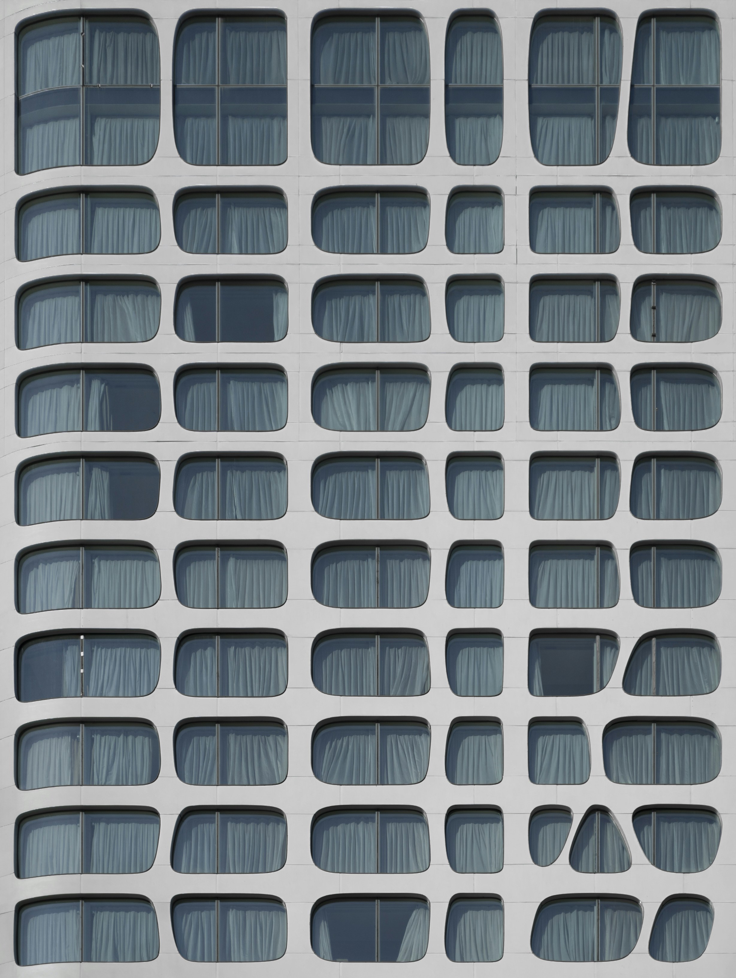 Abstract facade of a modern building featuring a grid of rounded windows with sheer curtains.
