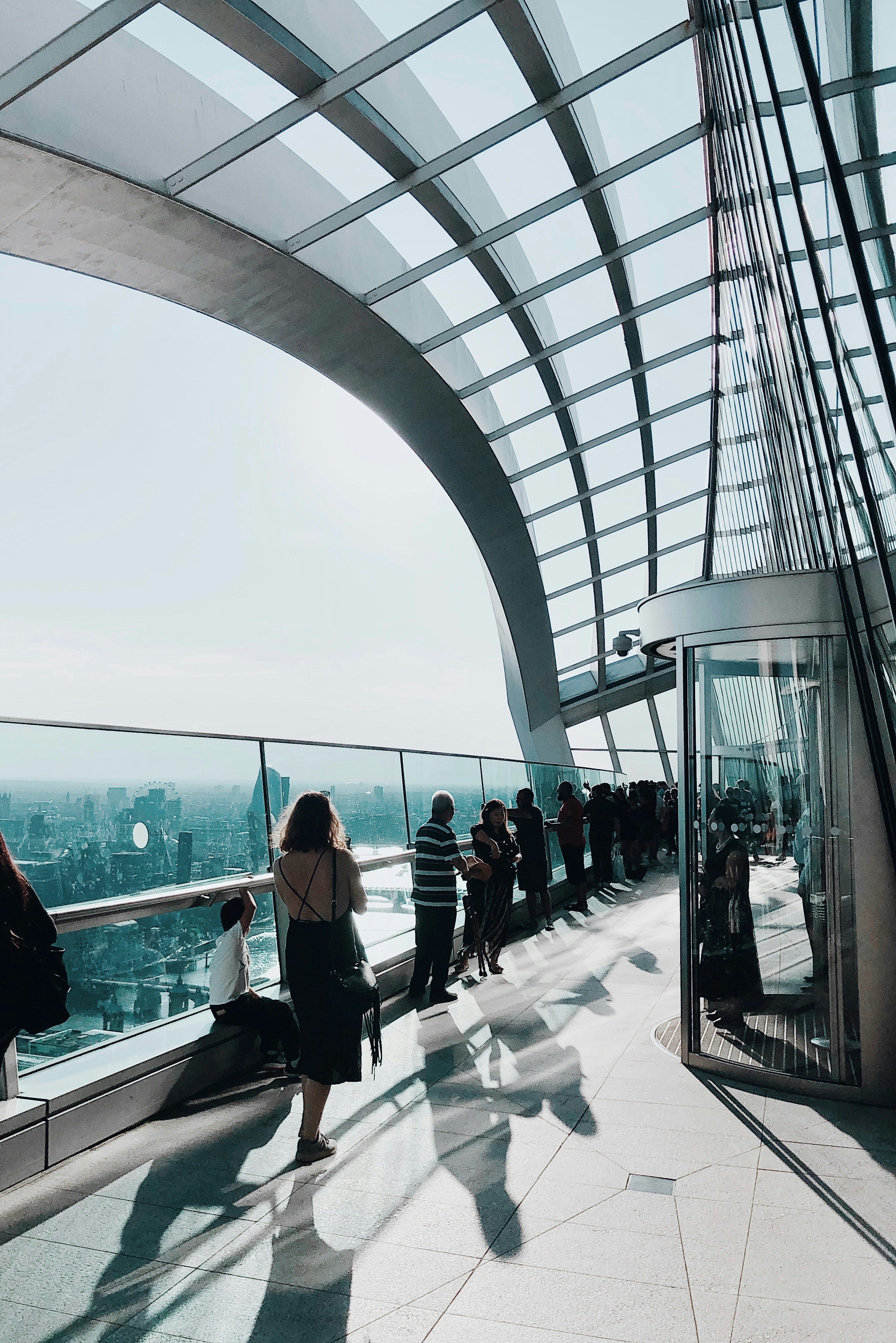 Visitors enjoying panoramic views from a modern observation deck, with a striking architectural design and elongated shadows cast on the floor.