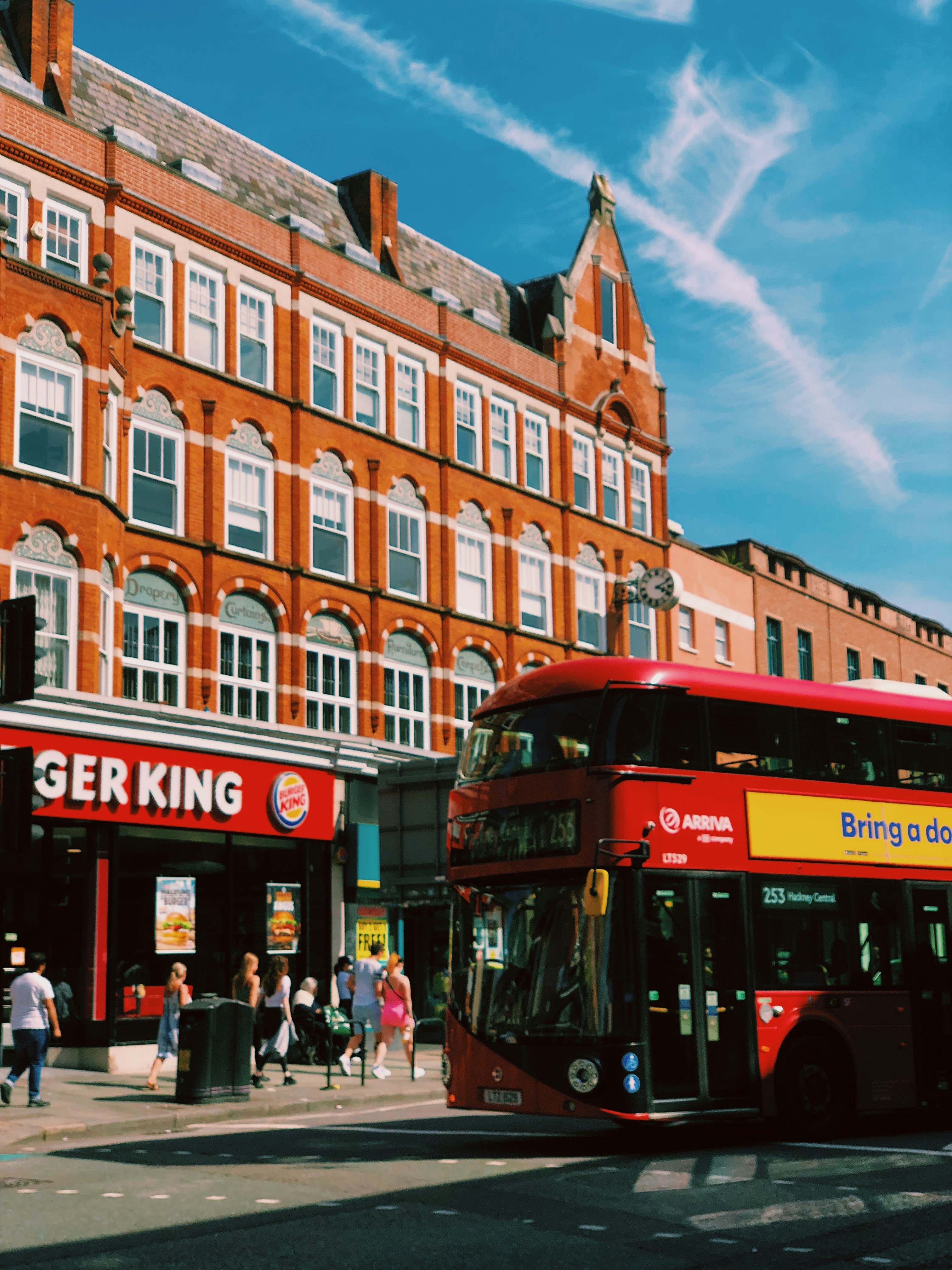 Red double-decker bus navigating a bustling street with historic brick buildings and fast-food outlets in view.