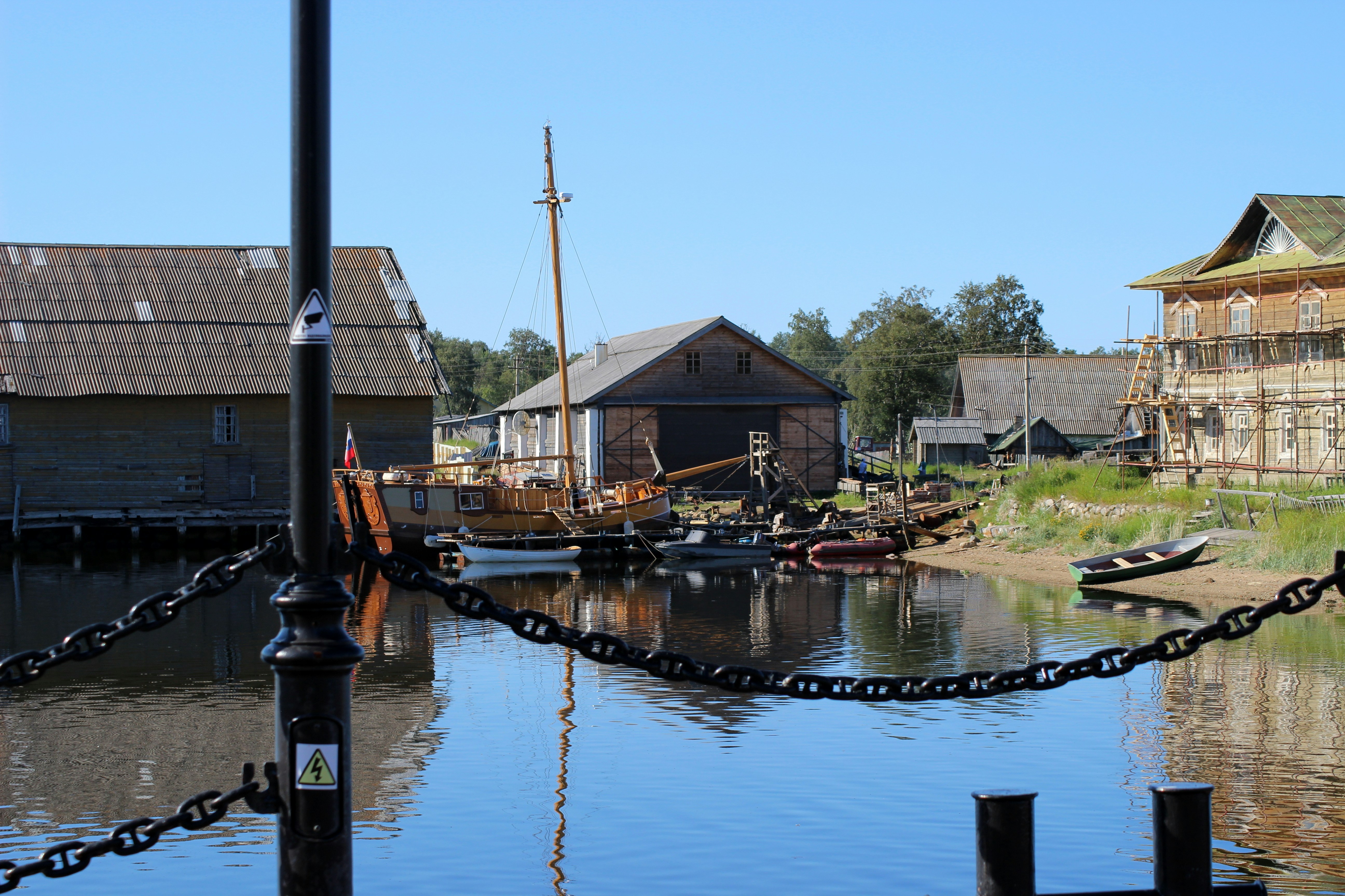 Historic wooden buildings and a traditional boat reflect in serene waters, capturing a moment of tranquility in a bygone era.