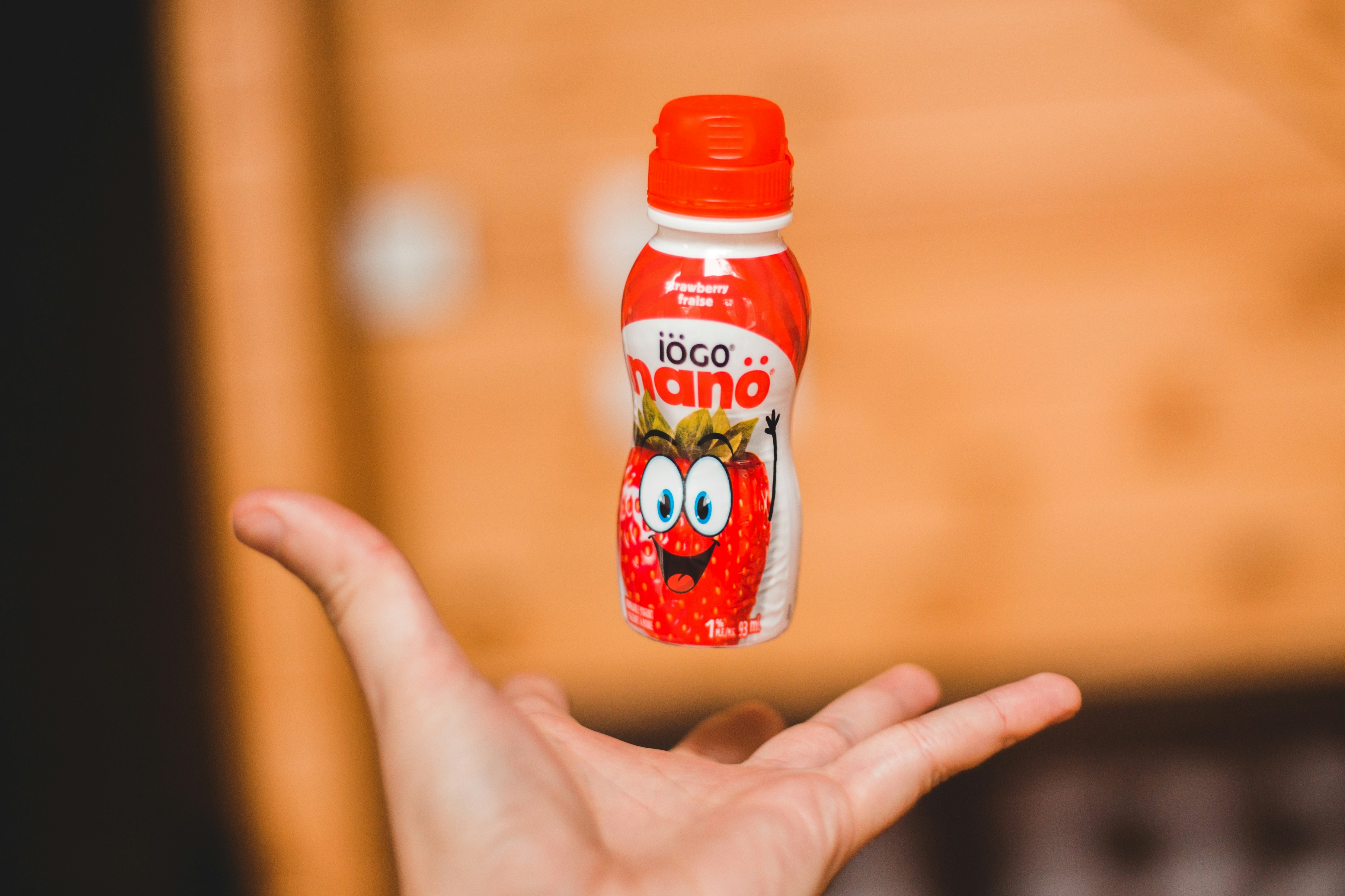 A playful bottle of strawberry-flavored yogurt drink hovers above an outstretched hand, showcasing its cartoonish design and vibrant colors.