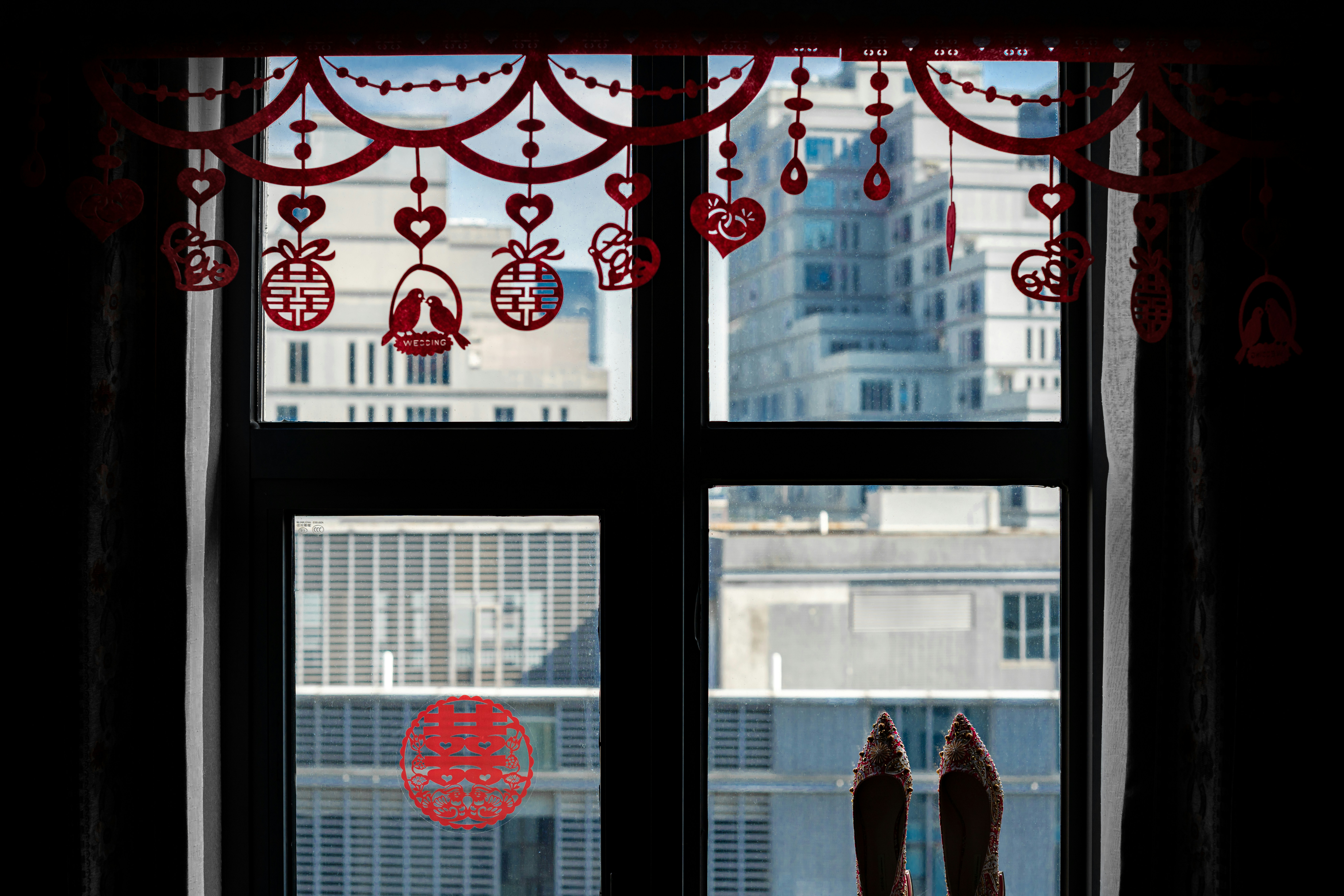 Two Feet at the Window: Festive Red Ornaments Framing a Distant Cityscape