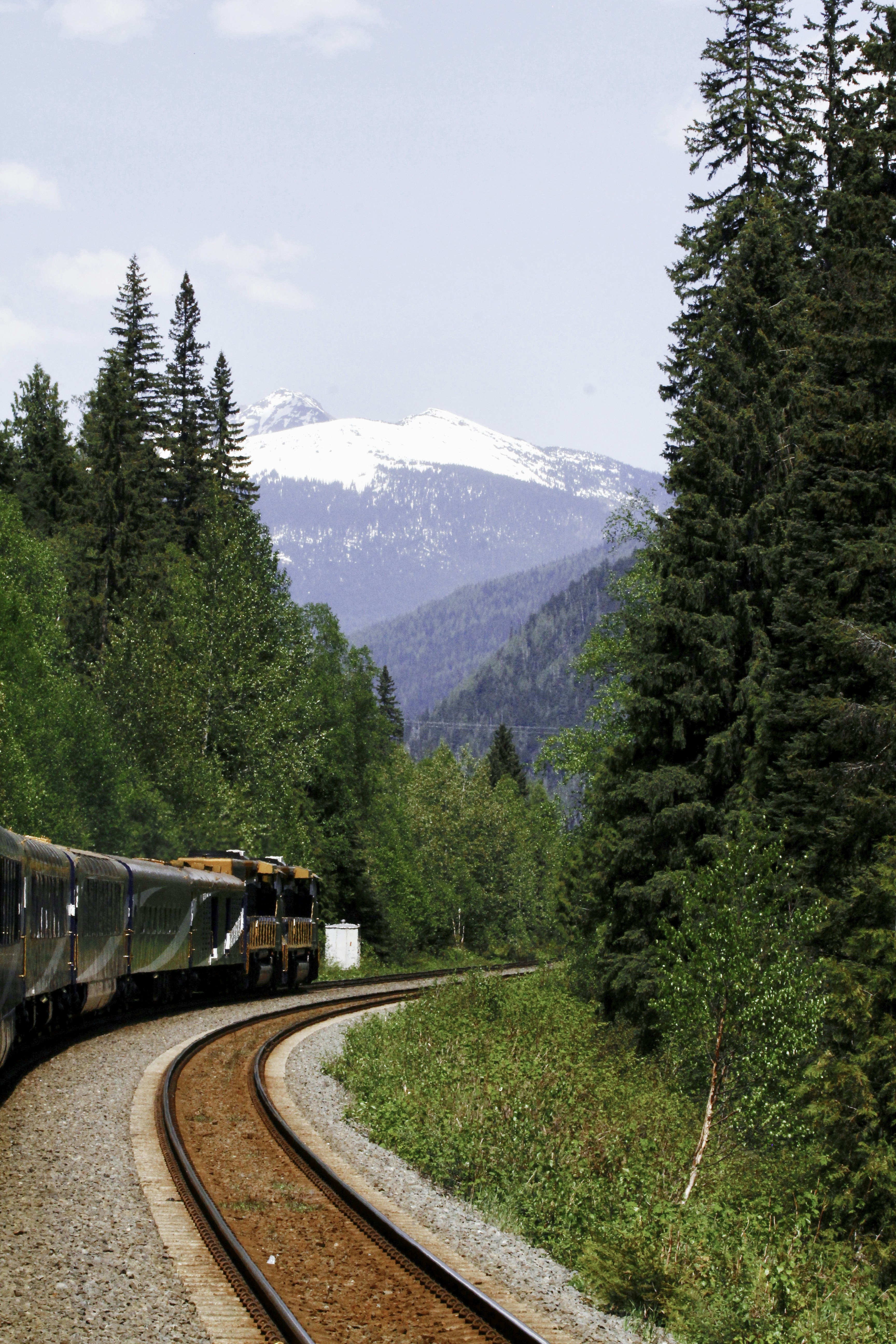 Curved Rails through a Green Corridor toward Snow-Capped Peaks