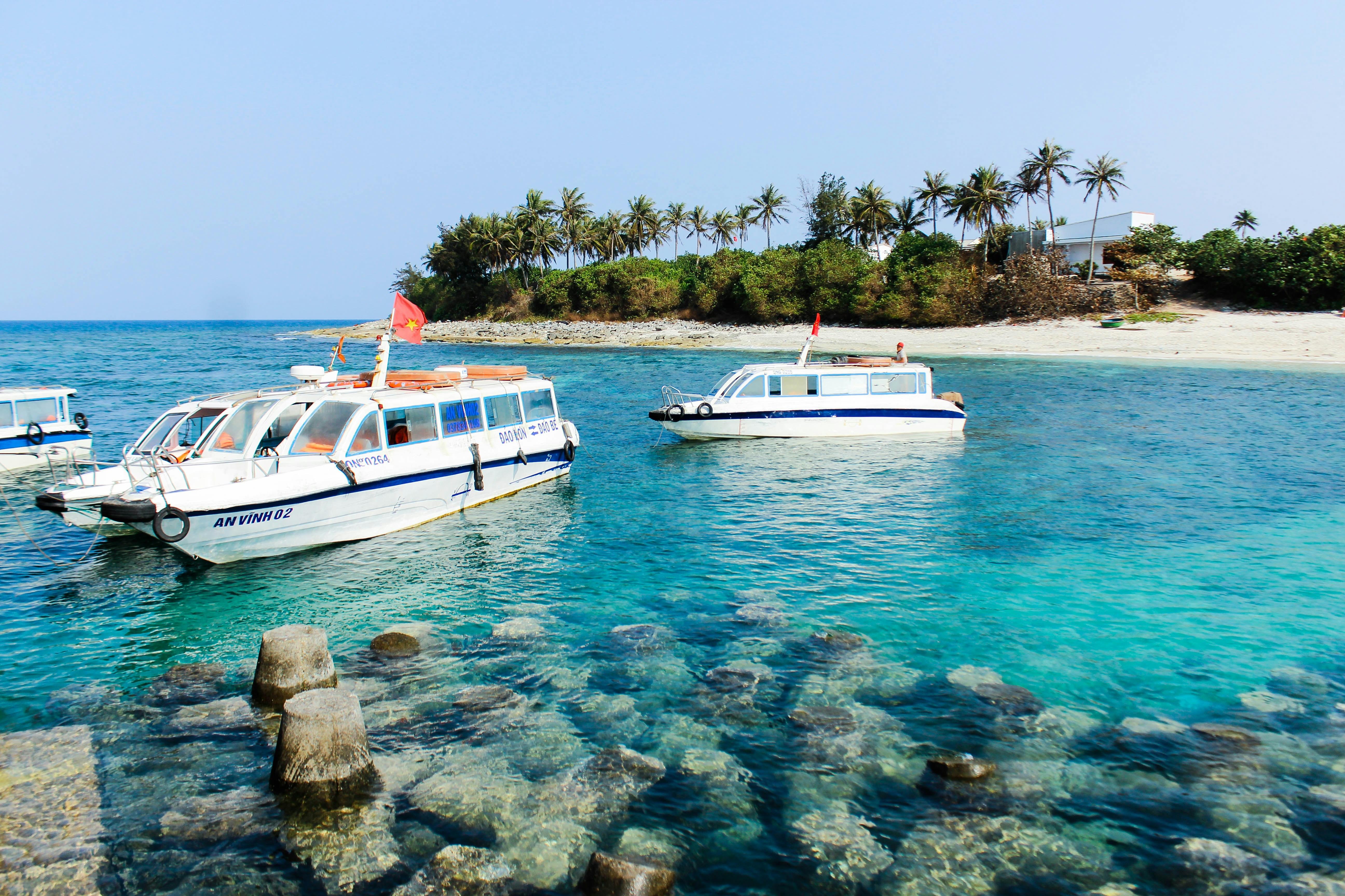 White boats float on clear turquoise waters near a palm-fringed island under a bright sky.