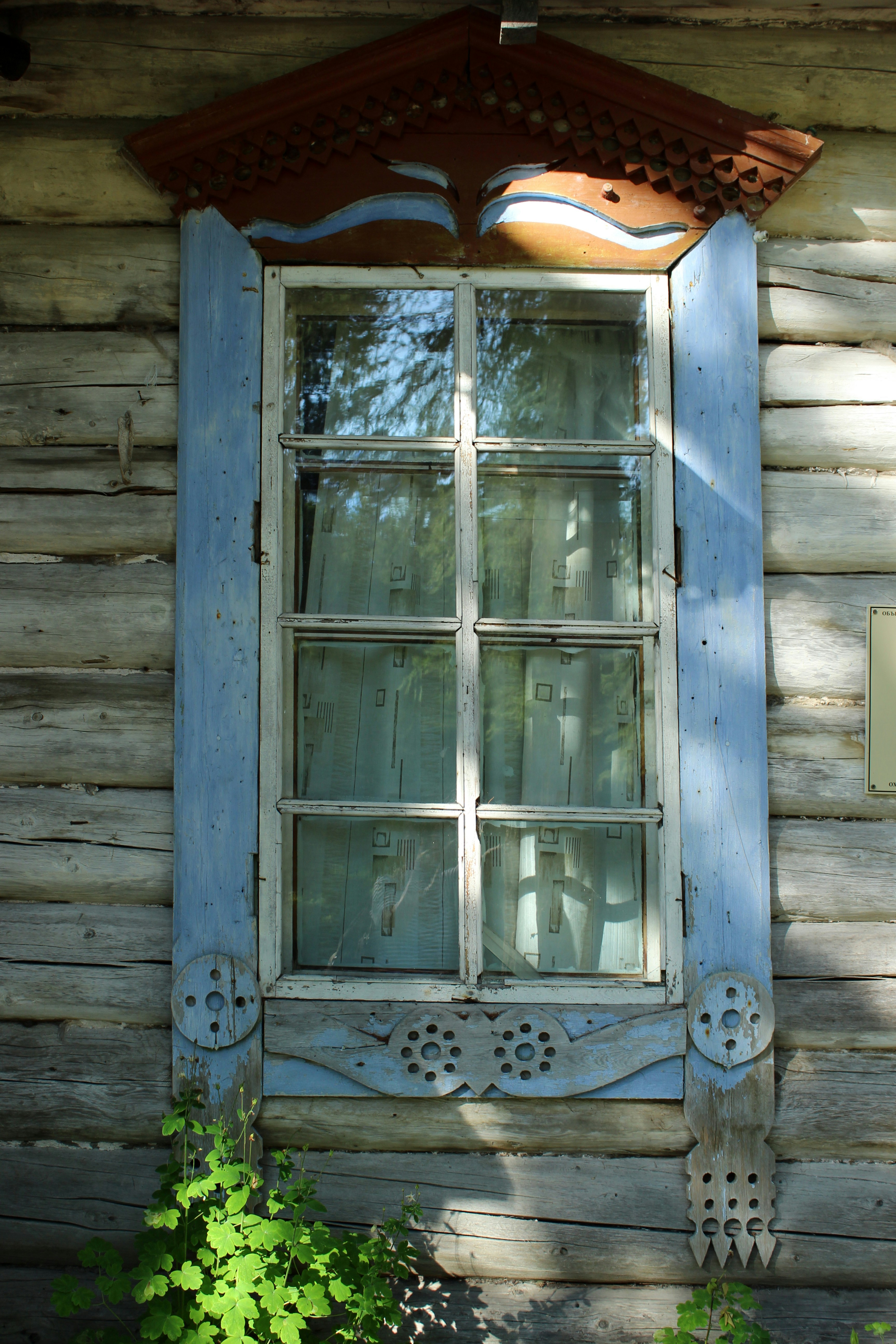 Intricately carved wooden window frame adorned with blue paint, set against a rustic log wall, capturing the essence of traditional craftsmanship.