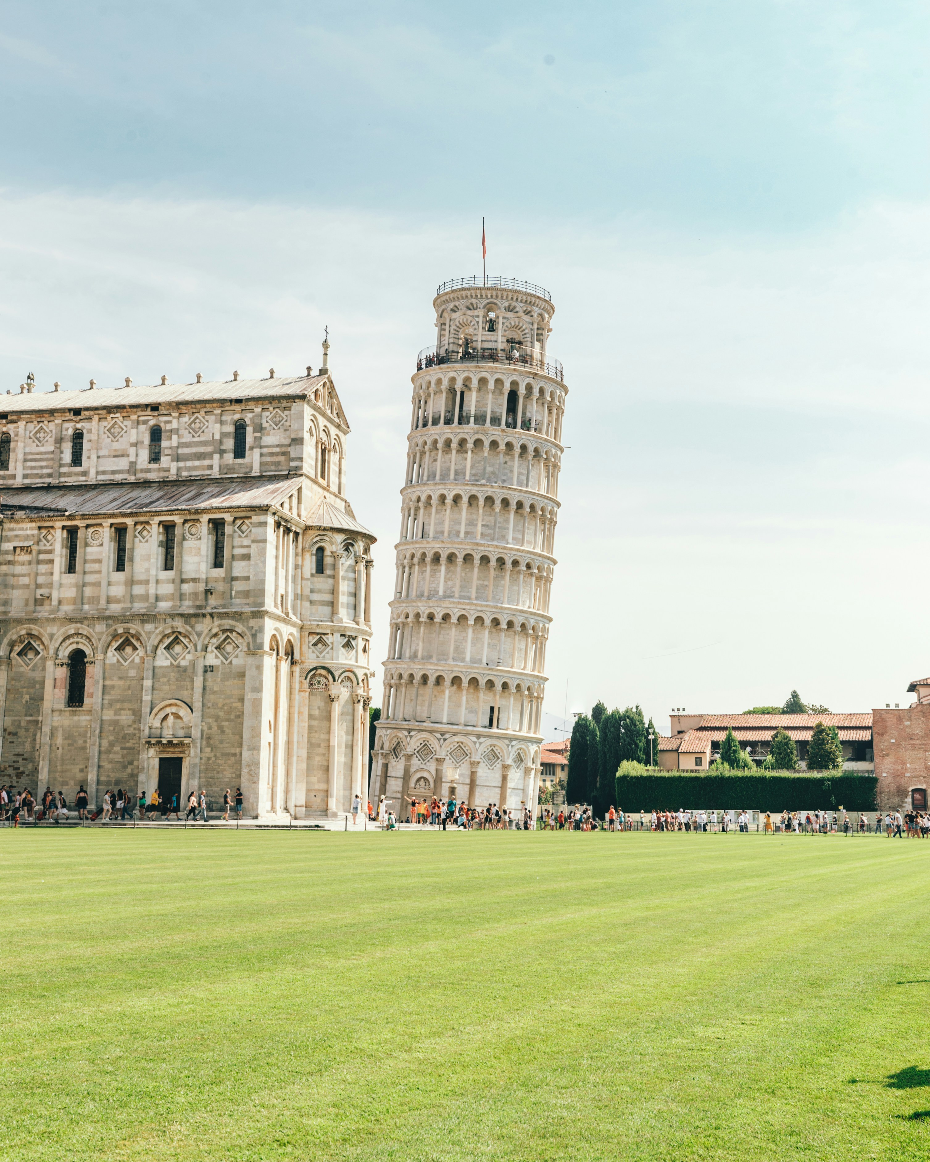 The Leaning Tower of Pisa stands beside the Pisa Cathedral, showcasing their architectural grandeur against a clear sky.