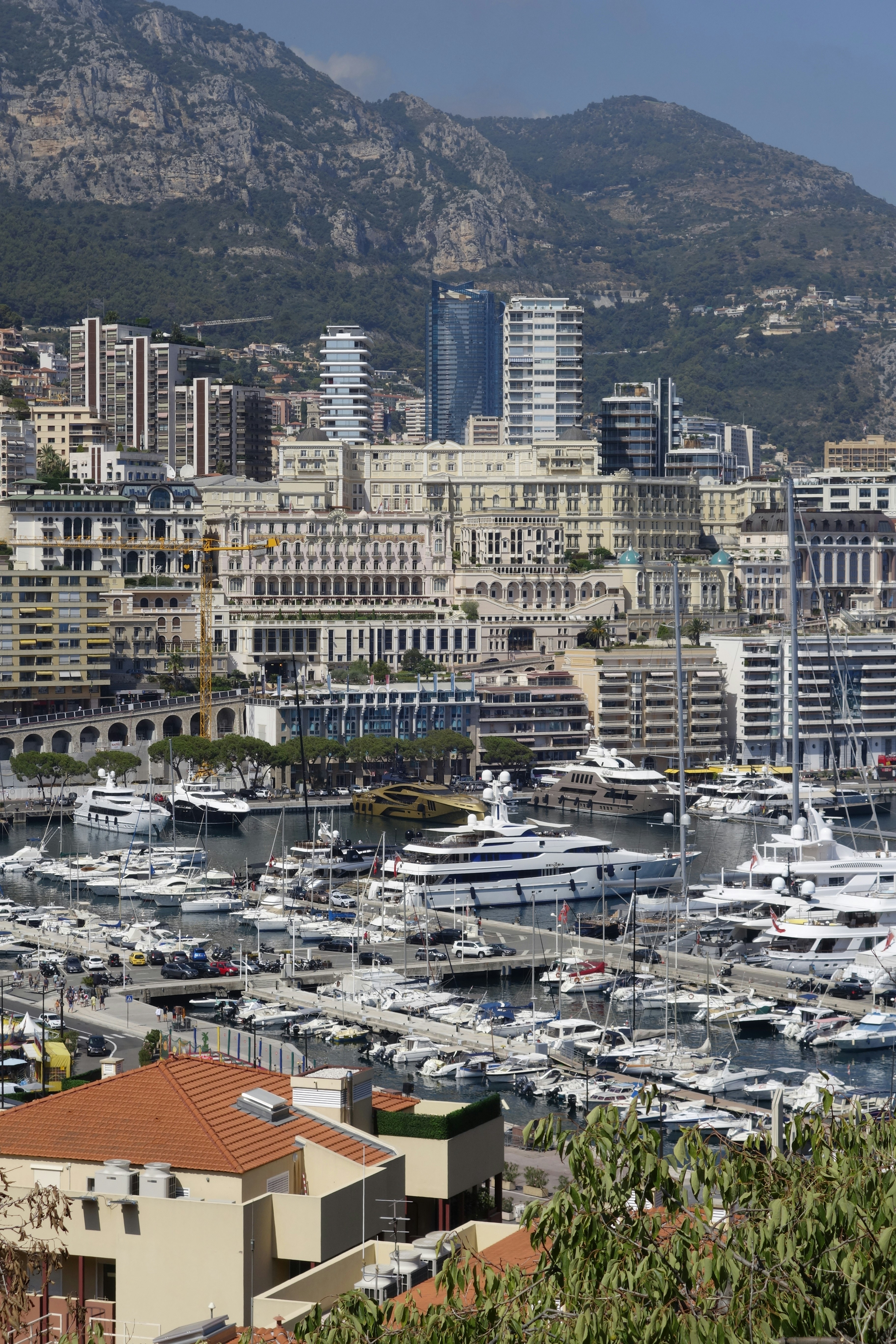 Vibrant marina filled with luxurious yachts, framed by modern and historic buildings in Monaco's picturesque harbor. The backdrop features the majestic mountains.