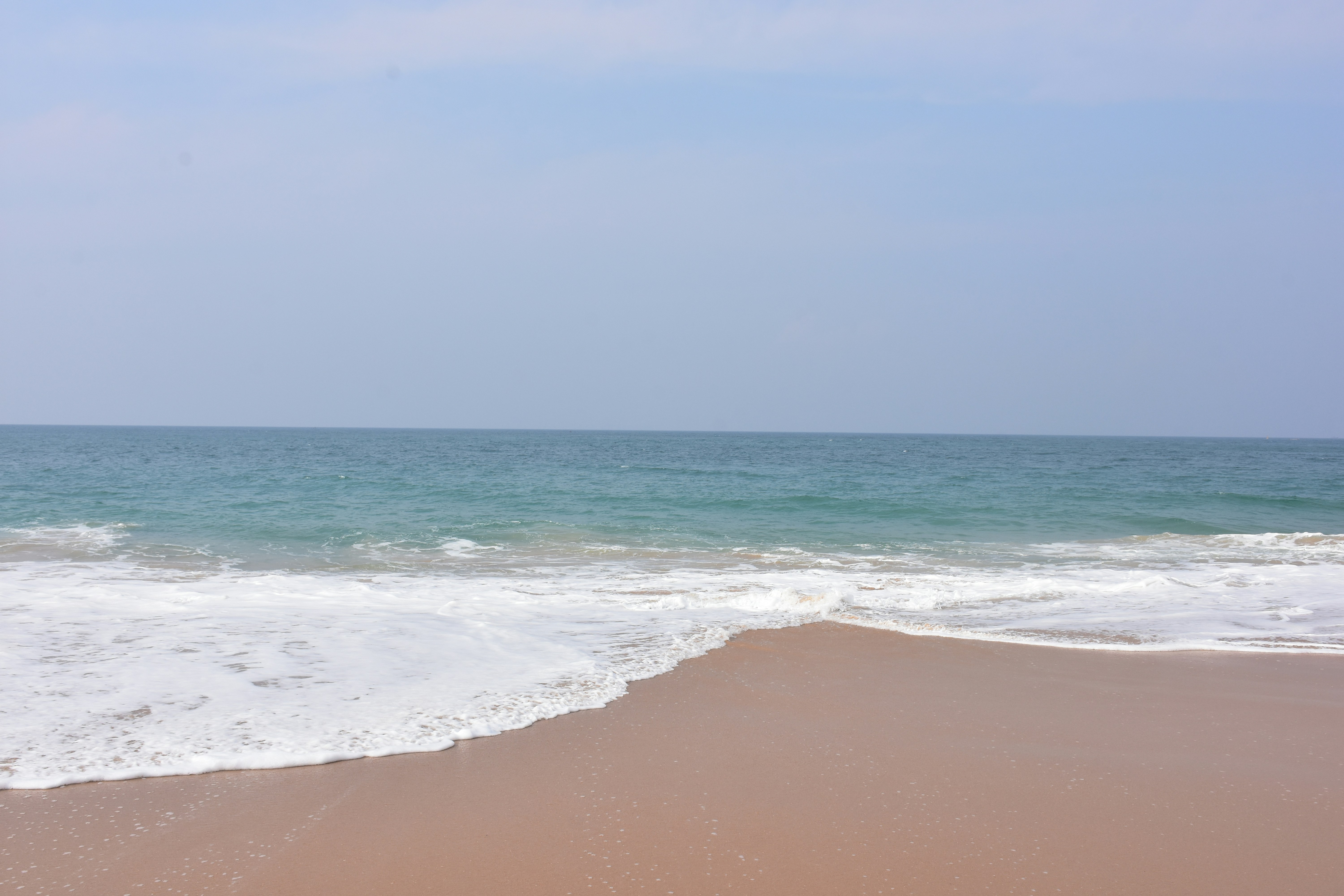 Gentle waves lapping against a sandy shore under a clear blue sky.