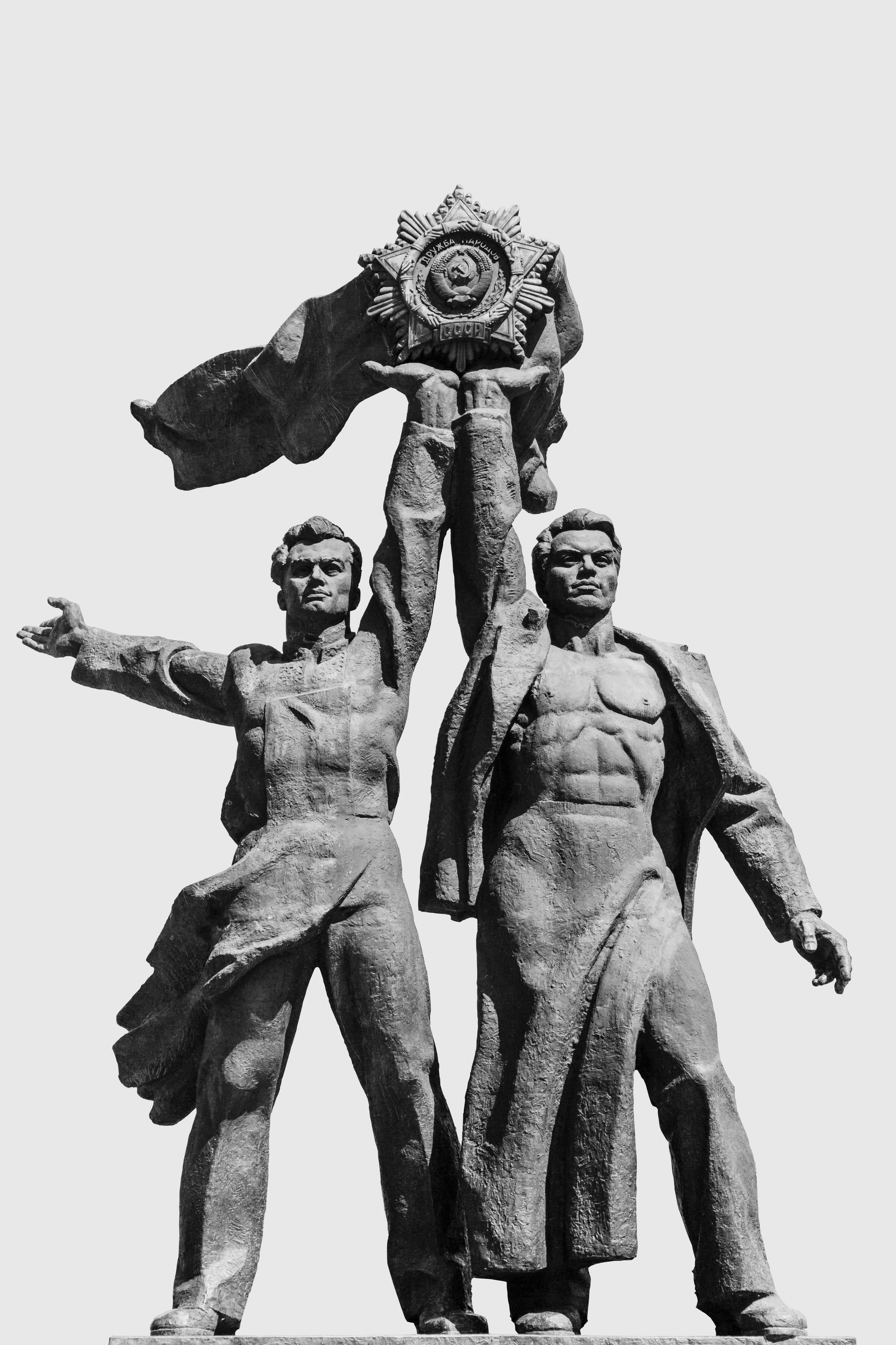 Two strong figures in bronze, one holding a radiant emblem aloft, embodying resilience and solidarity. The sculpture captures a moment of triumph and strength.