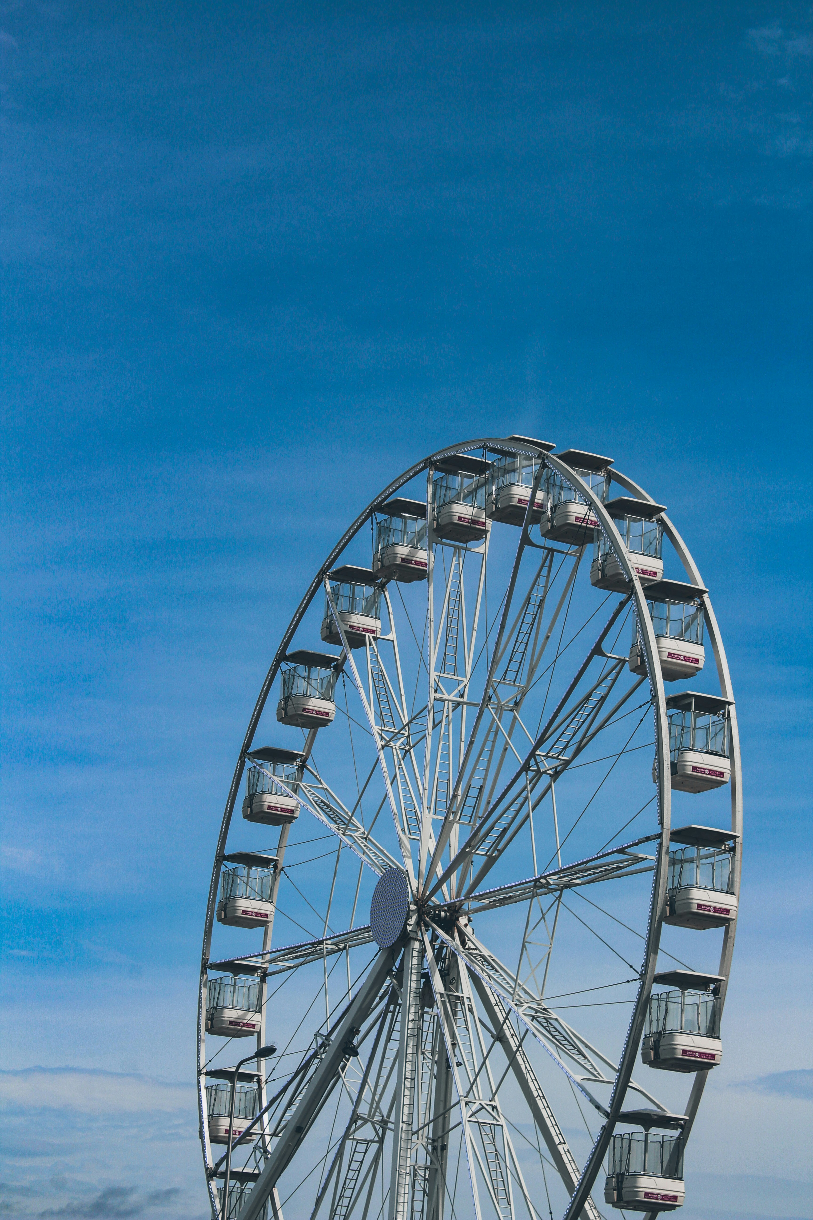 A towering Ferris wheel spins against a bright blue sky, showcasing its vibrant gondolas. The scene captures the essence of fun and leisure.