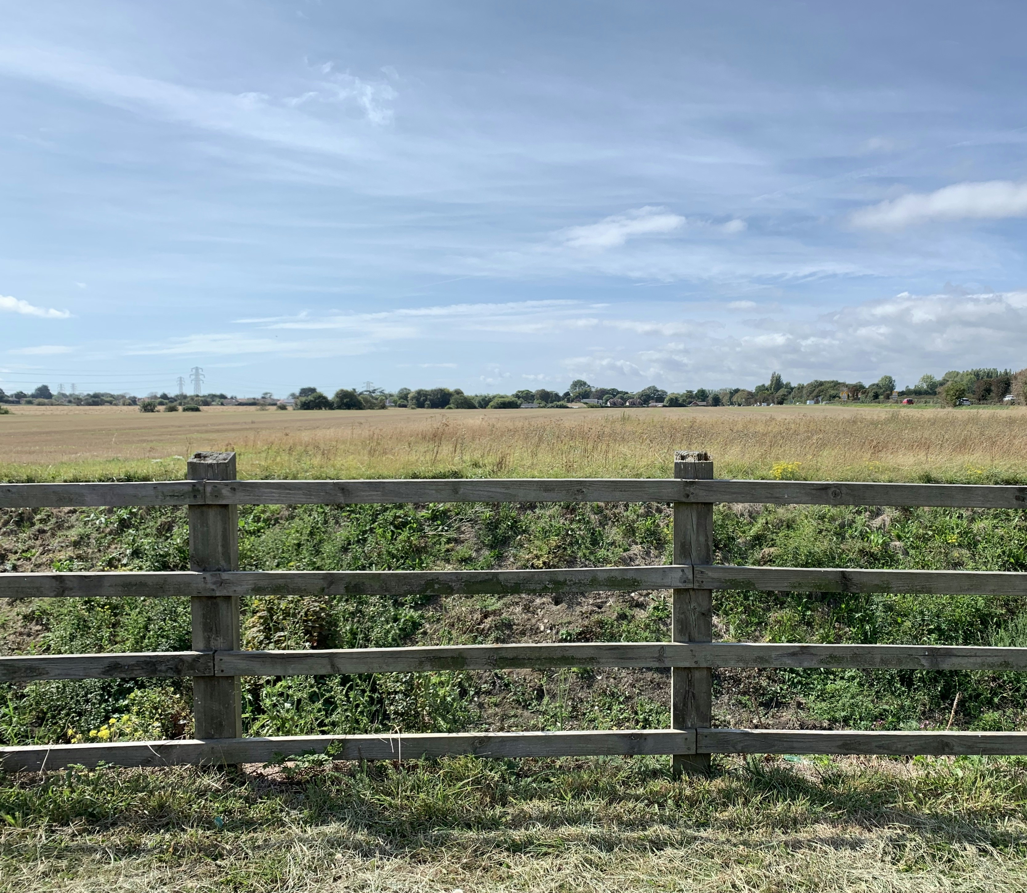 Wooden fence overlooking a vast grassy field under a clear blue sky.