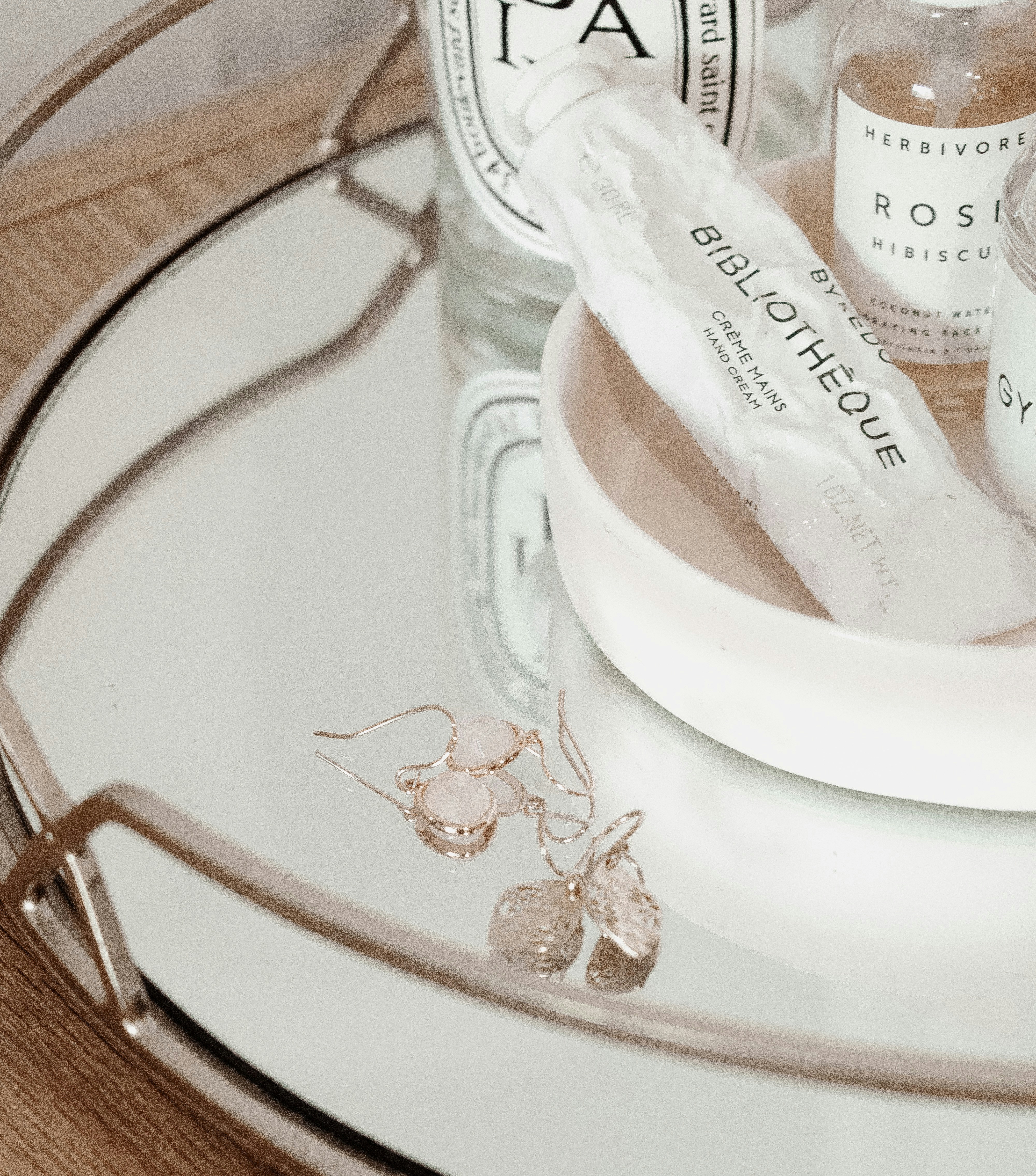 A collection of beauty products and delicate jewelry arranged on a mirrored tray, highlighting elegance and simplicity.