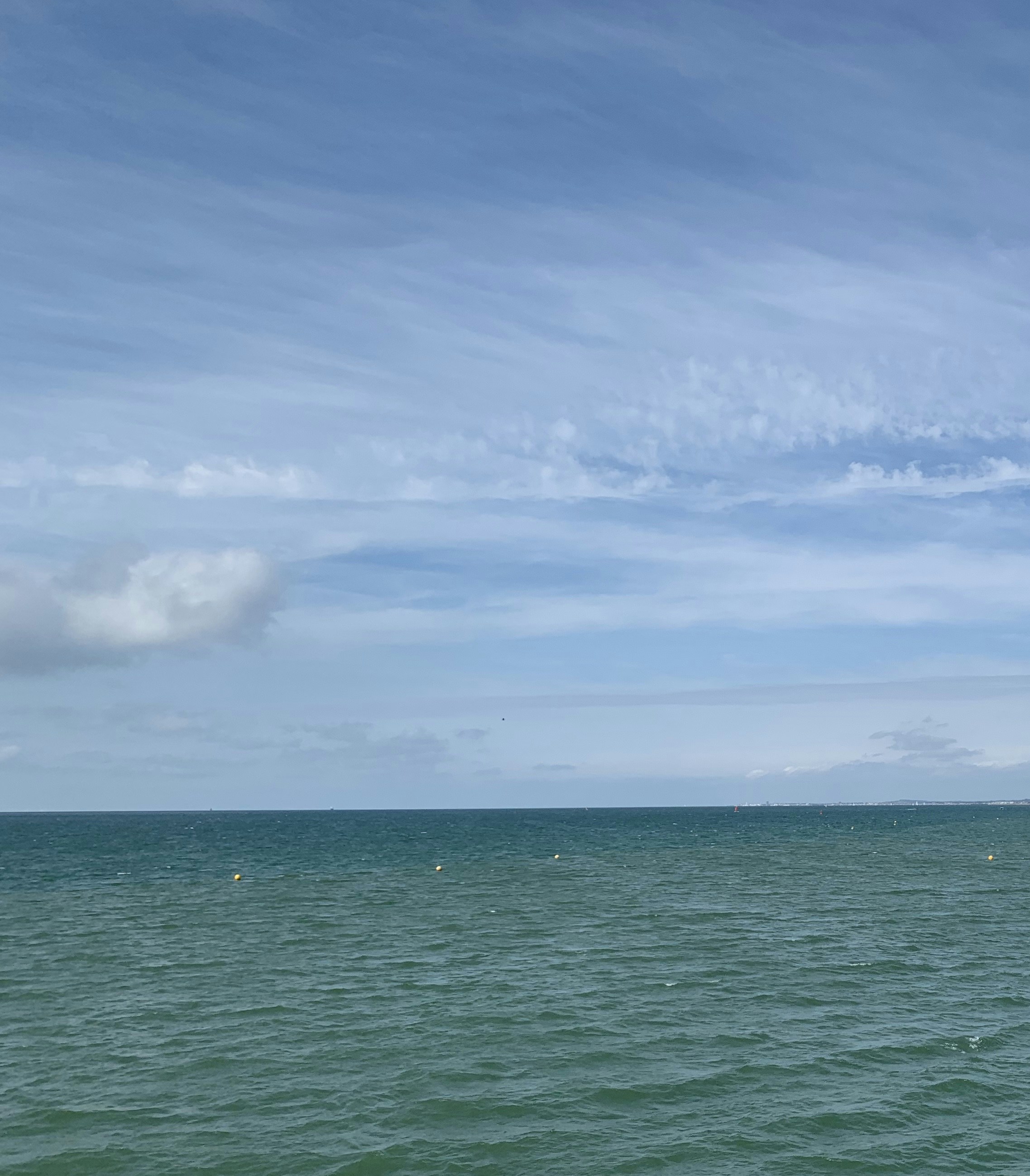 Vast expanse of calm ocean under a lightly clouded sky, with gentle waves creating a serene atmosphere.