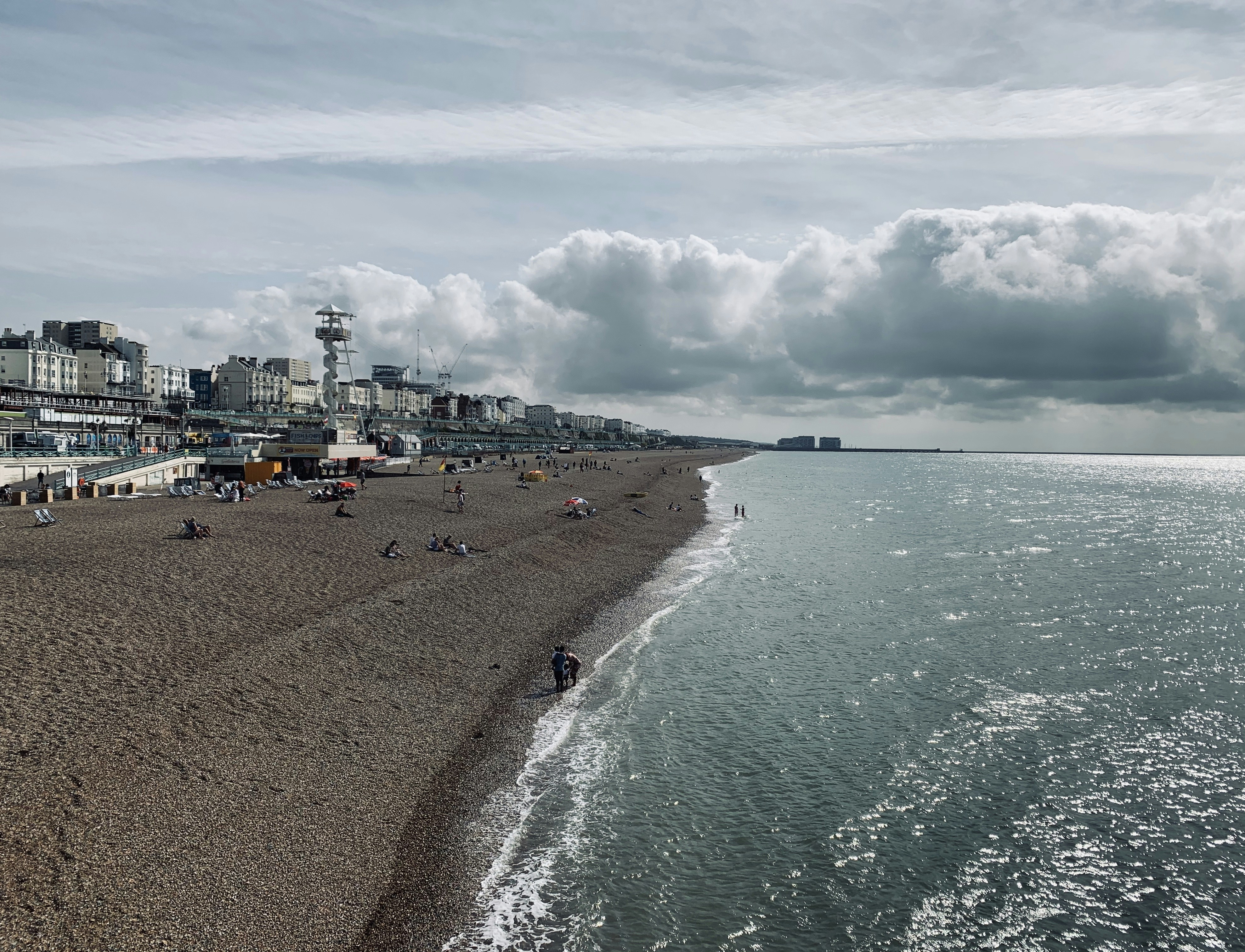 Expansive beach meets calm sea under a sky filled with dramatic clouds.