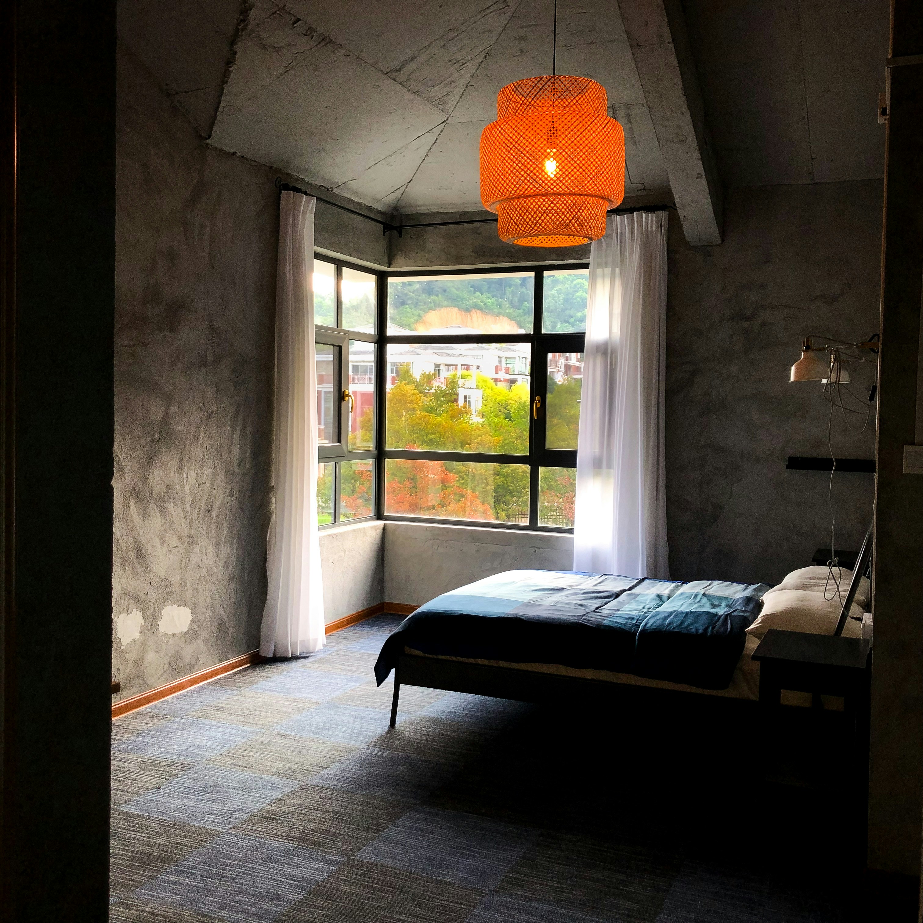 Bedroom with a large window showcasing vibrant fall foliage, illuminated by a warm pendant light.