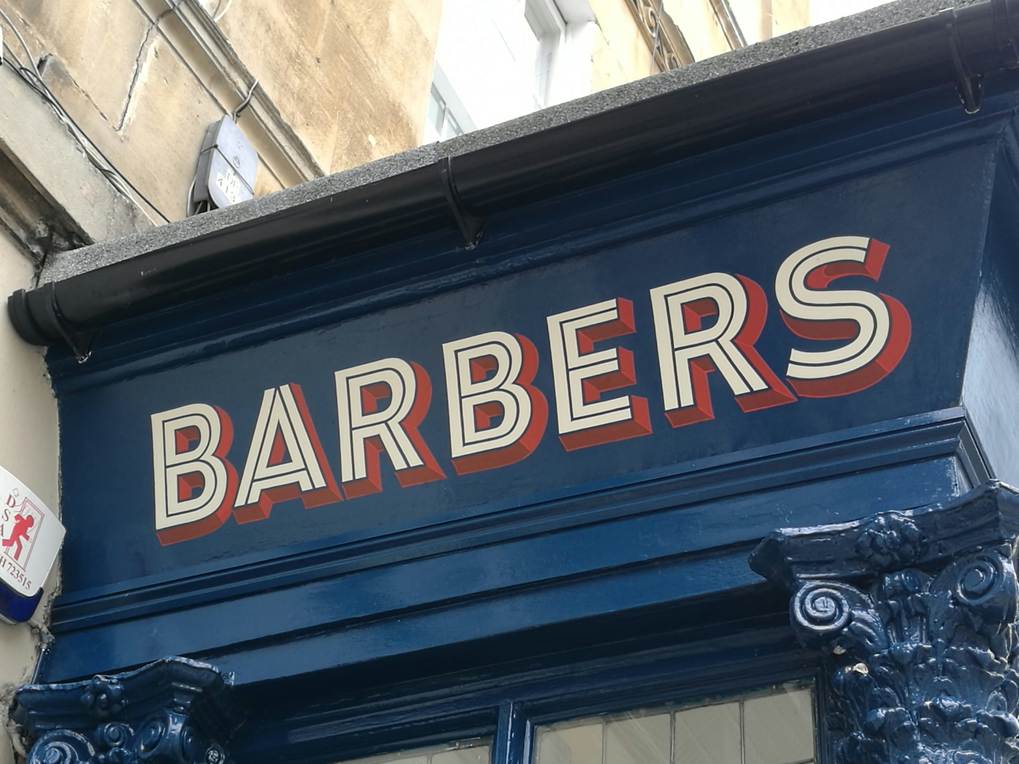 Boldly lettered 'BARBERS' sign on a vintage shopfront, showcasing classic design elements and rich blue hues.