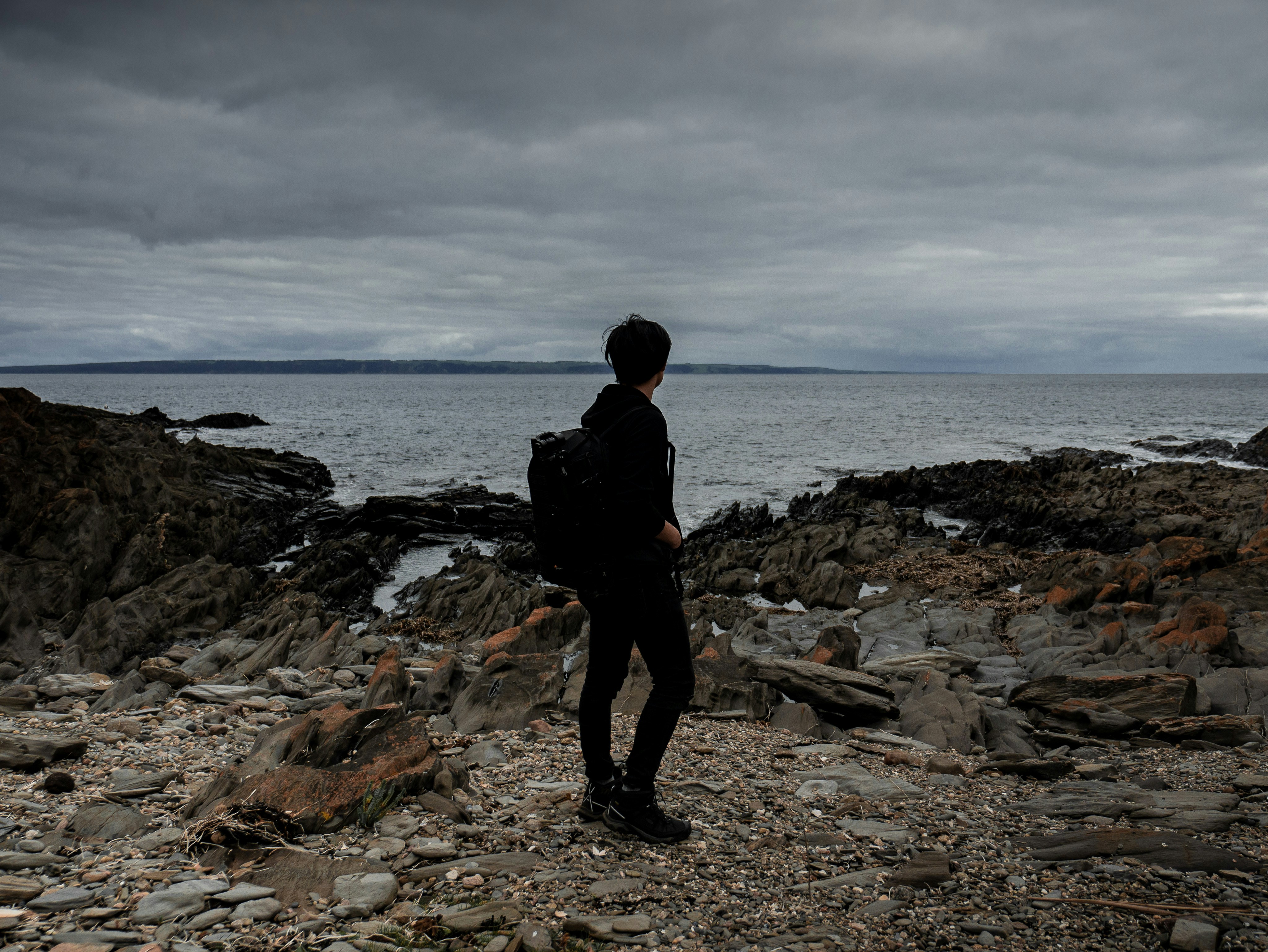 Lone Hiker at the Edge of a Rugged Coast under a Moody Sky