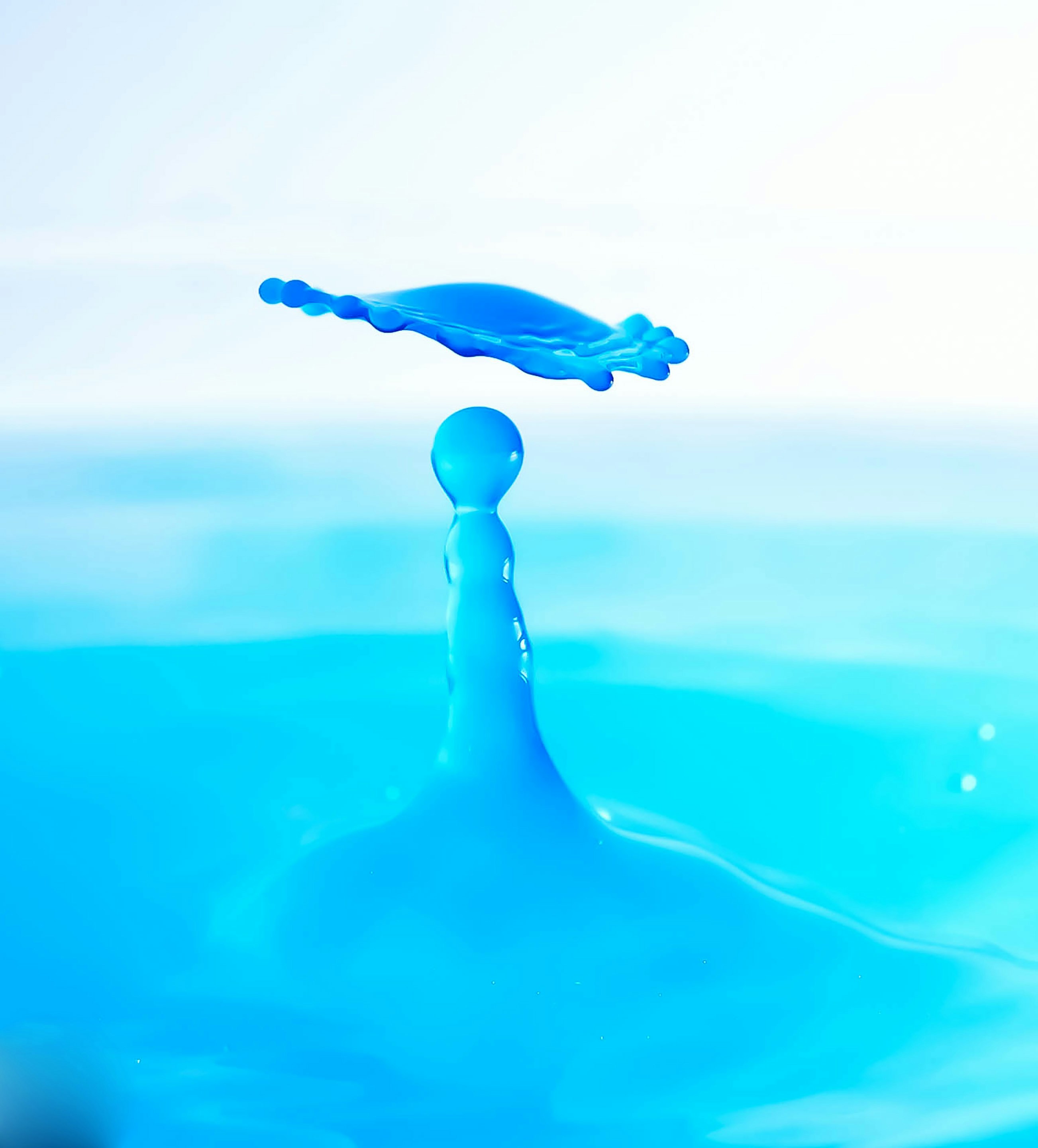 Blue water droplet creating a splash above a calm surface, showcasing the beauty of fluid dynamics.