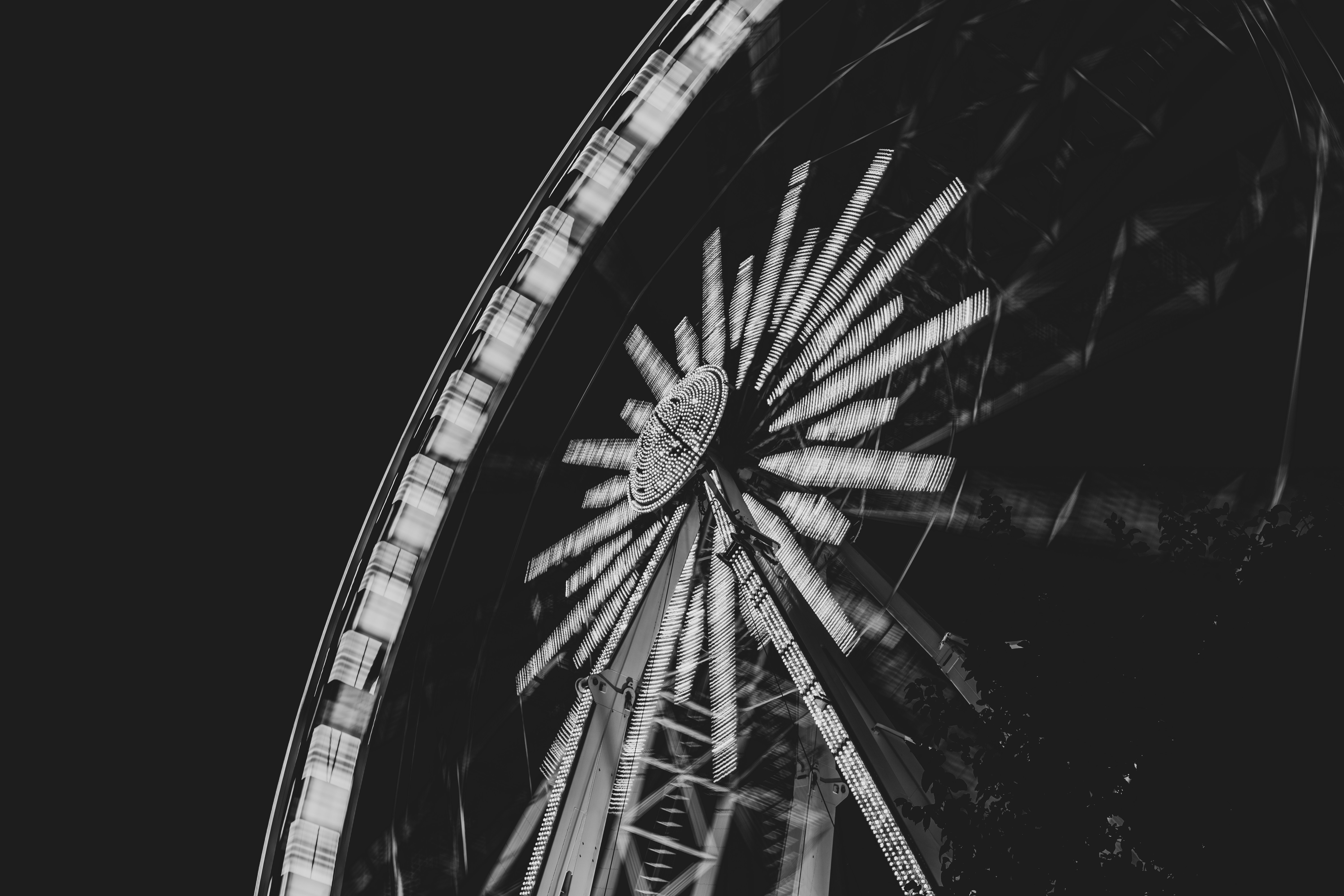 A dynamic black-and-white portrayal of a Ferris wheel in motion, capturing the interplay of light and shadow against the night sky.