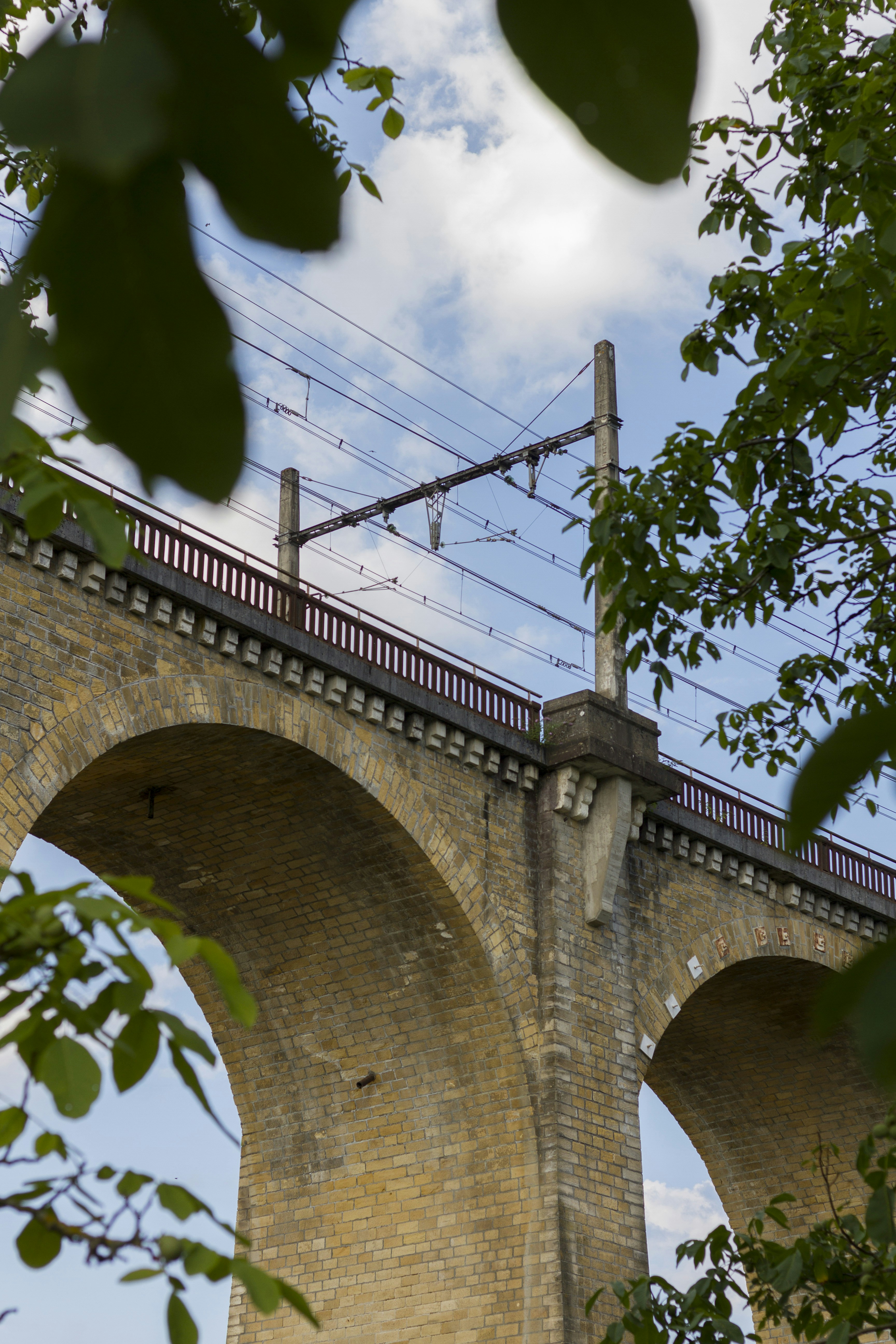 A stone viaduct with railway tracks overhead, framed by lush green foliage, showcasing the intersection of nature and engineering.