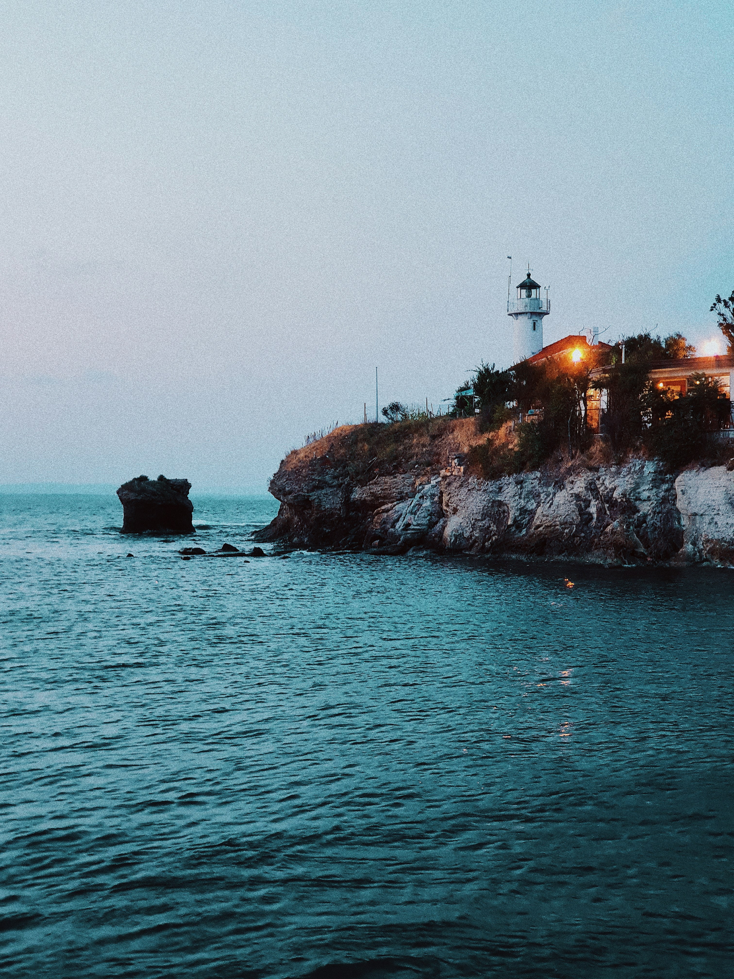 A lighthouse perched on a rocky coastline, illuminated against the soft hues of twilight, with gentle waves lapping at the shore.