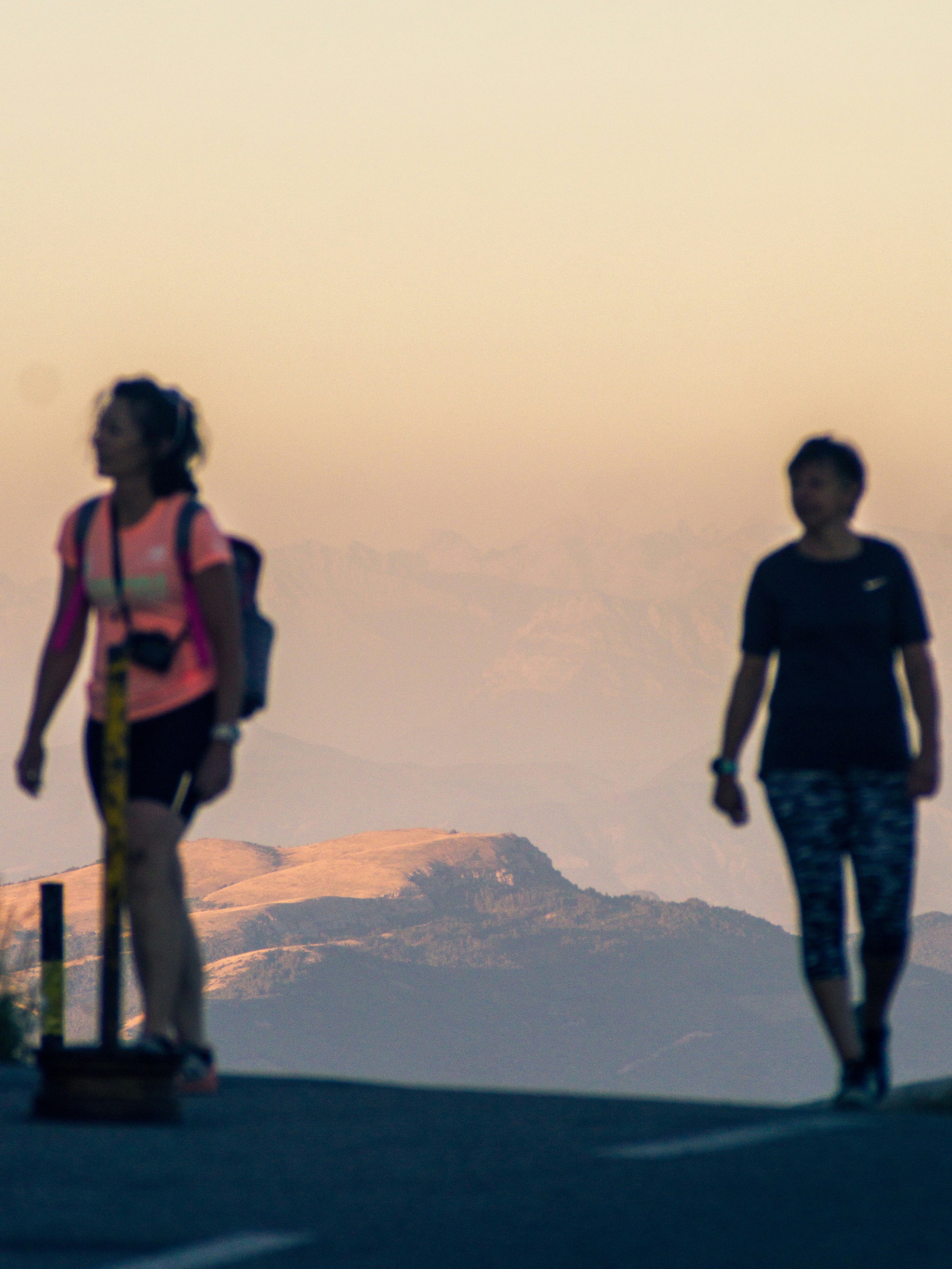 Two hikers walking along a road with a distant mountain range under a soft, hazy sky.