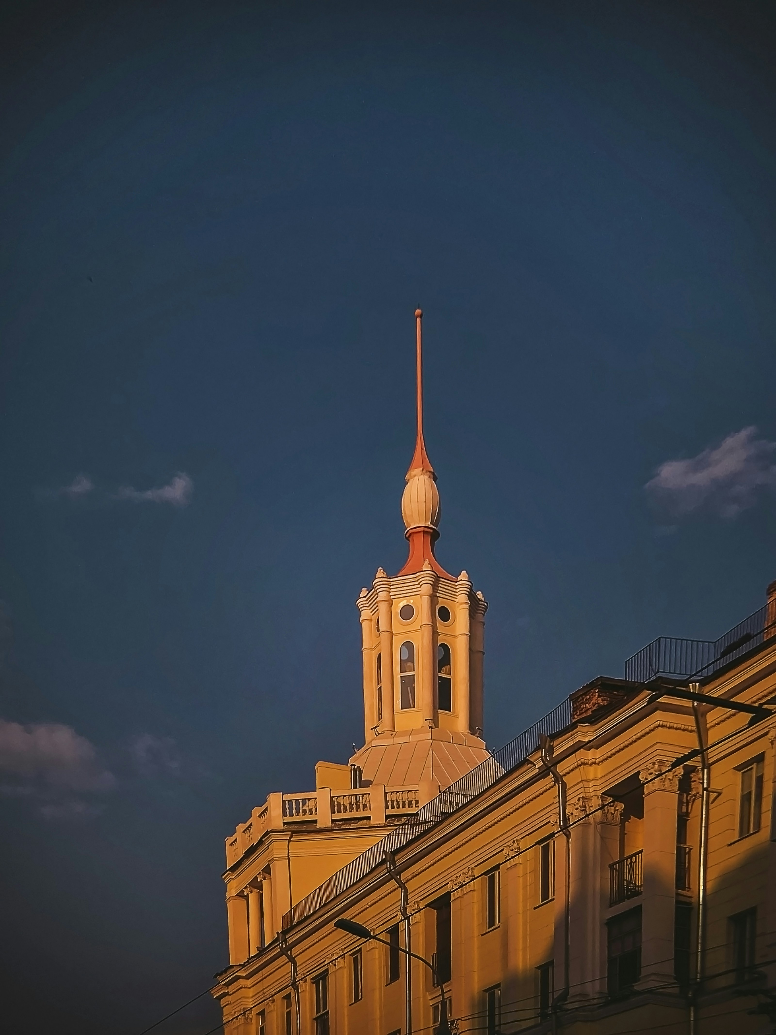 A historic building's ornate spire rises against a twilight sky, showcasing intricate design and warm lighting.