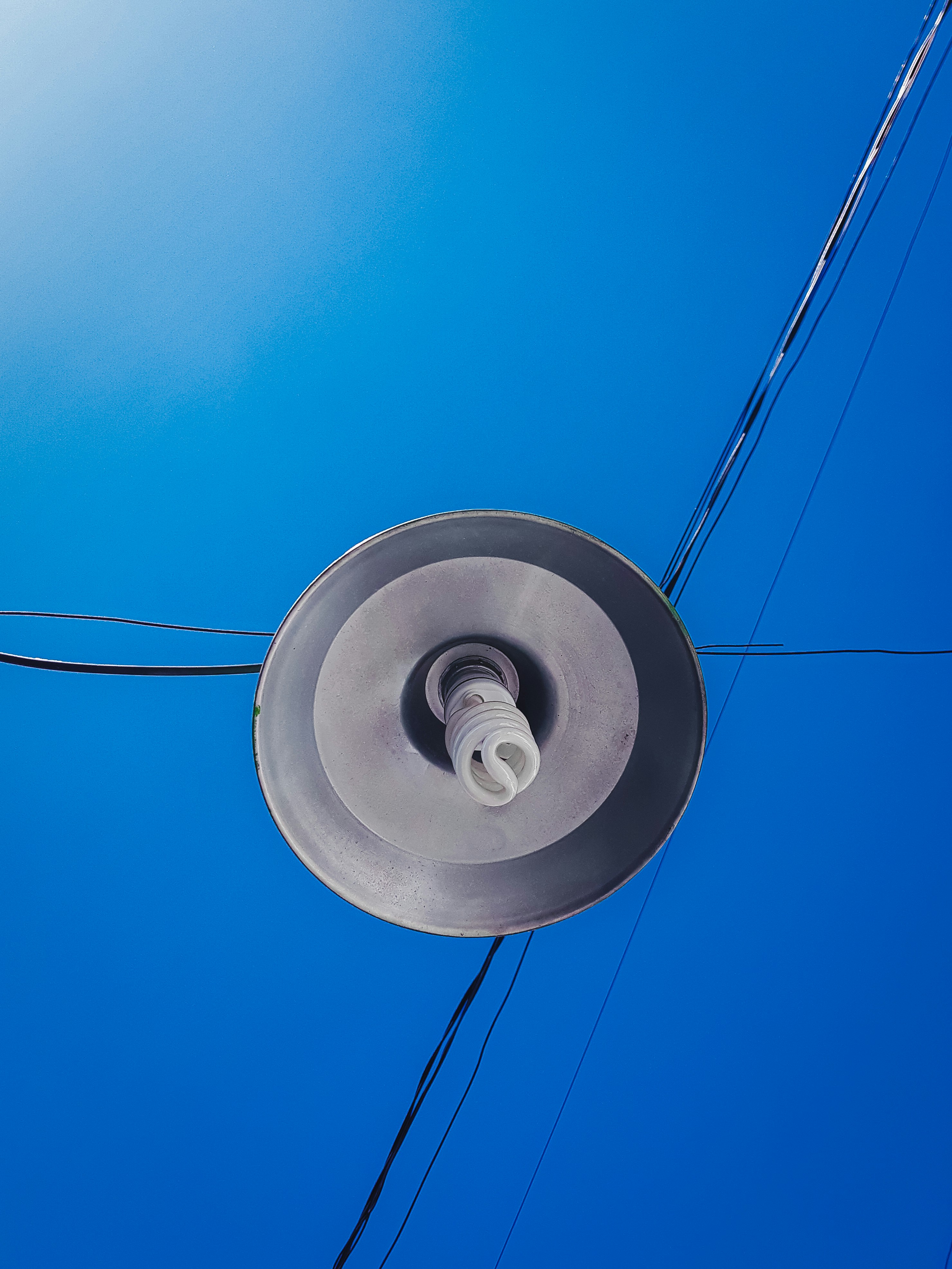 Close-up photograph of a circular streetlamp against a vivid blue sky with intersecting wires, creating geometric tension.