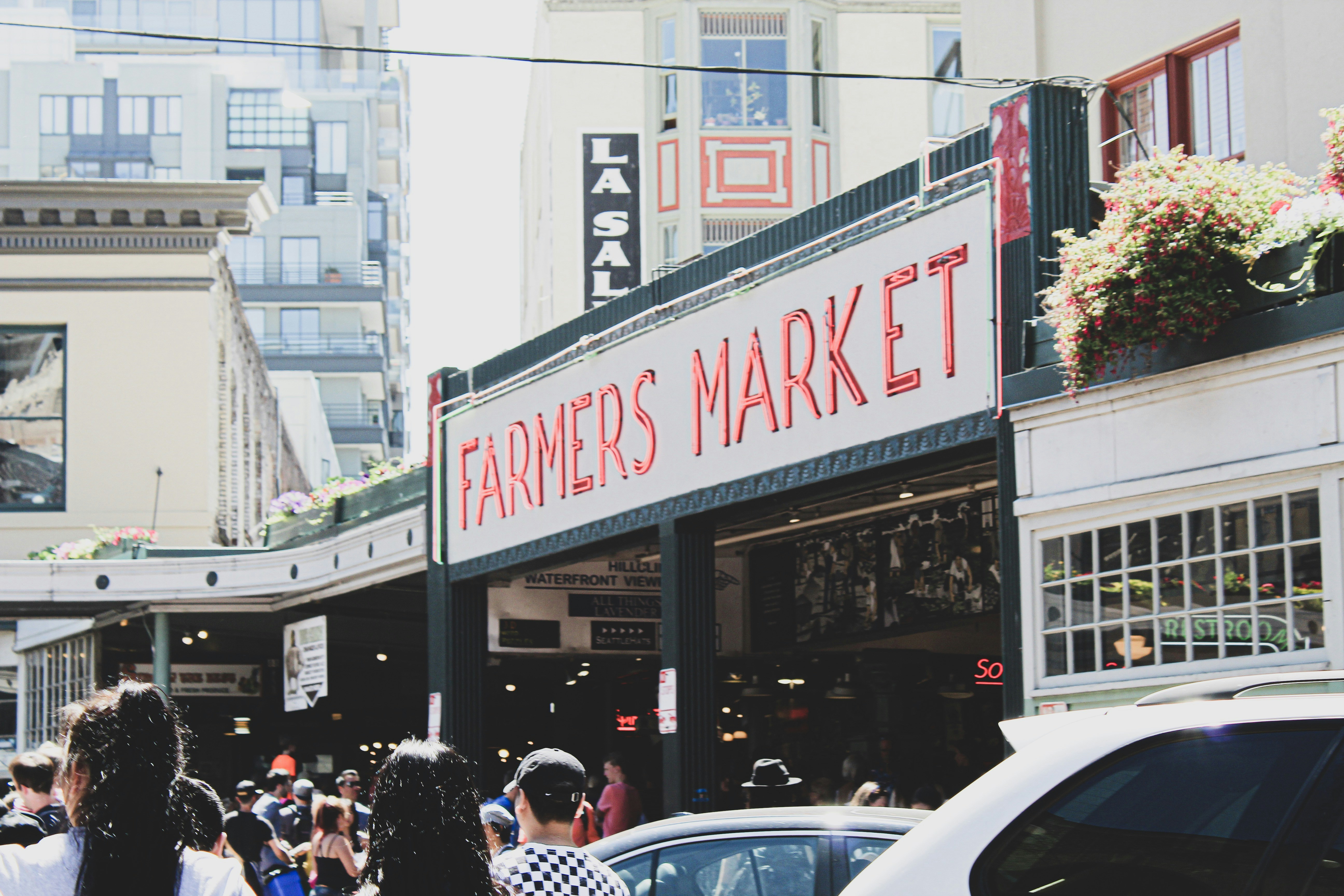 Bustling Market Front: Signage and Crowd at the Farmers Market Entrance