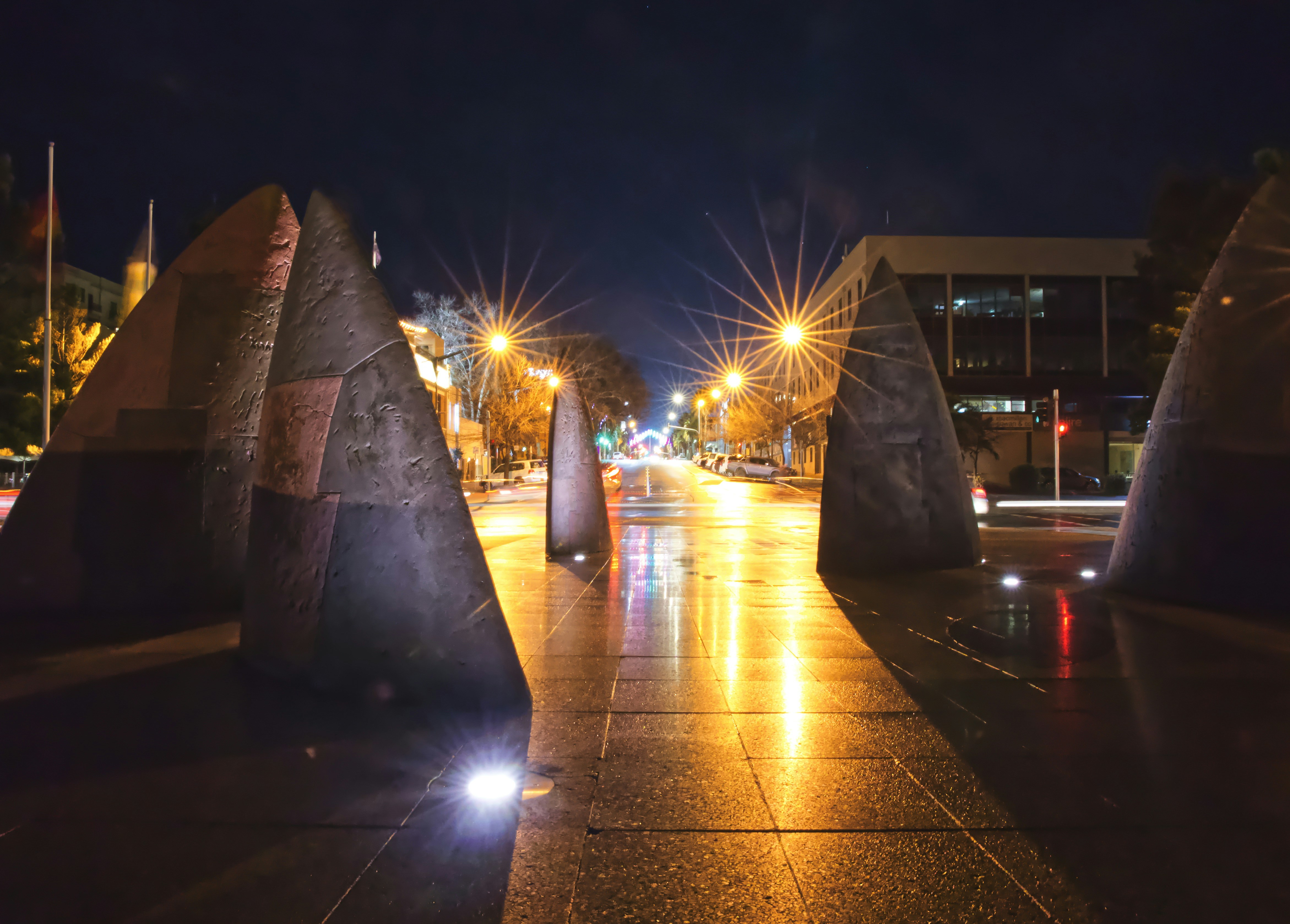 Illuminated stone structures line a wet city street under a starry night sky.