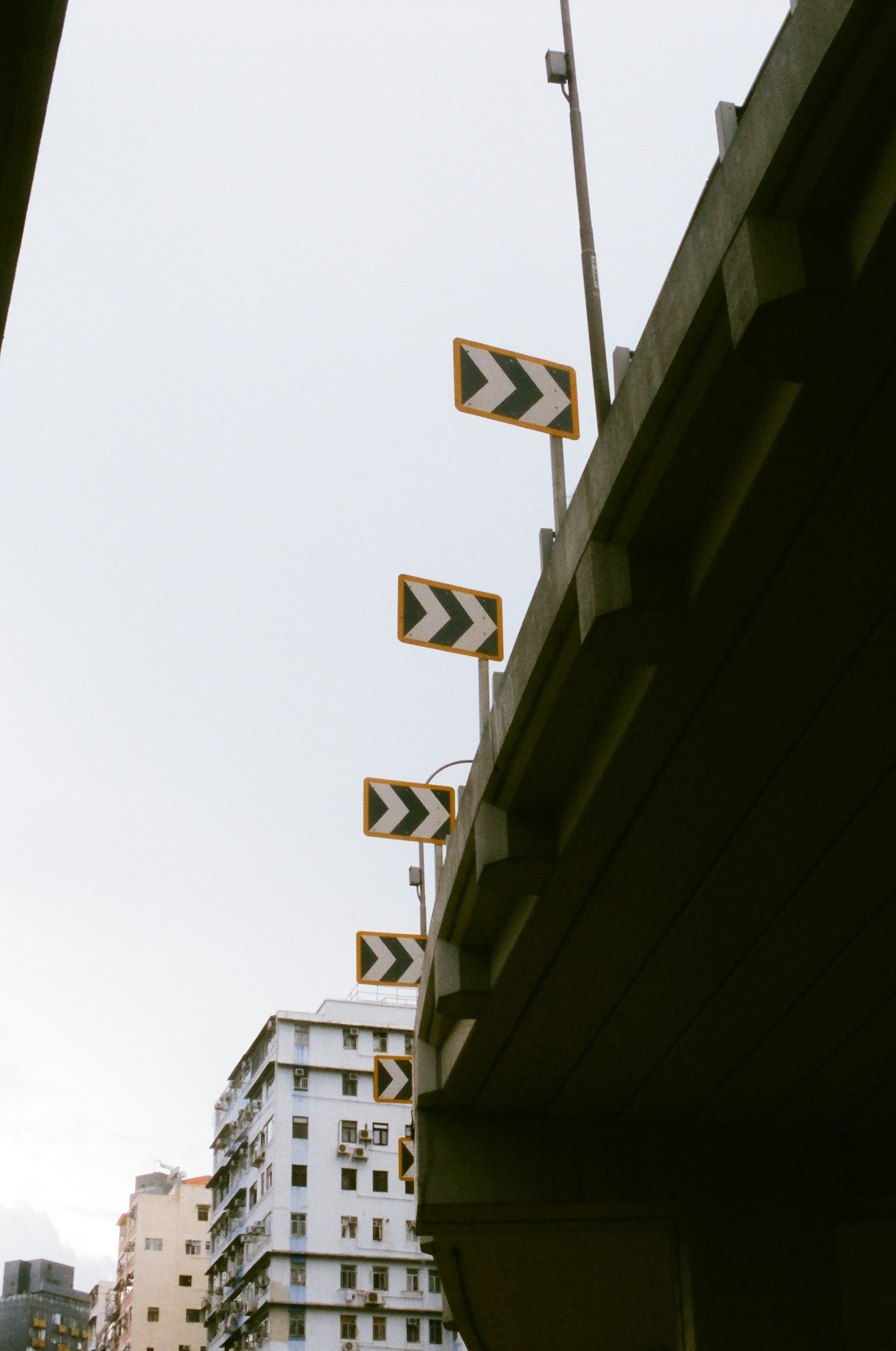 A series of directional signs mounted on a concrete overpass, juxtaposed against a backdrop of urban architecture. The scene captures the essence of city navigation.