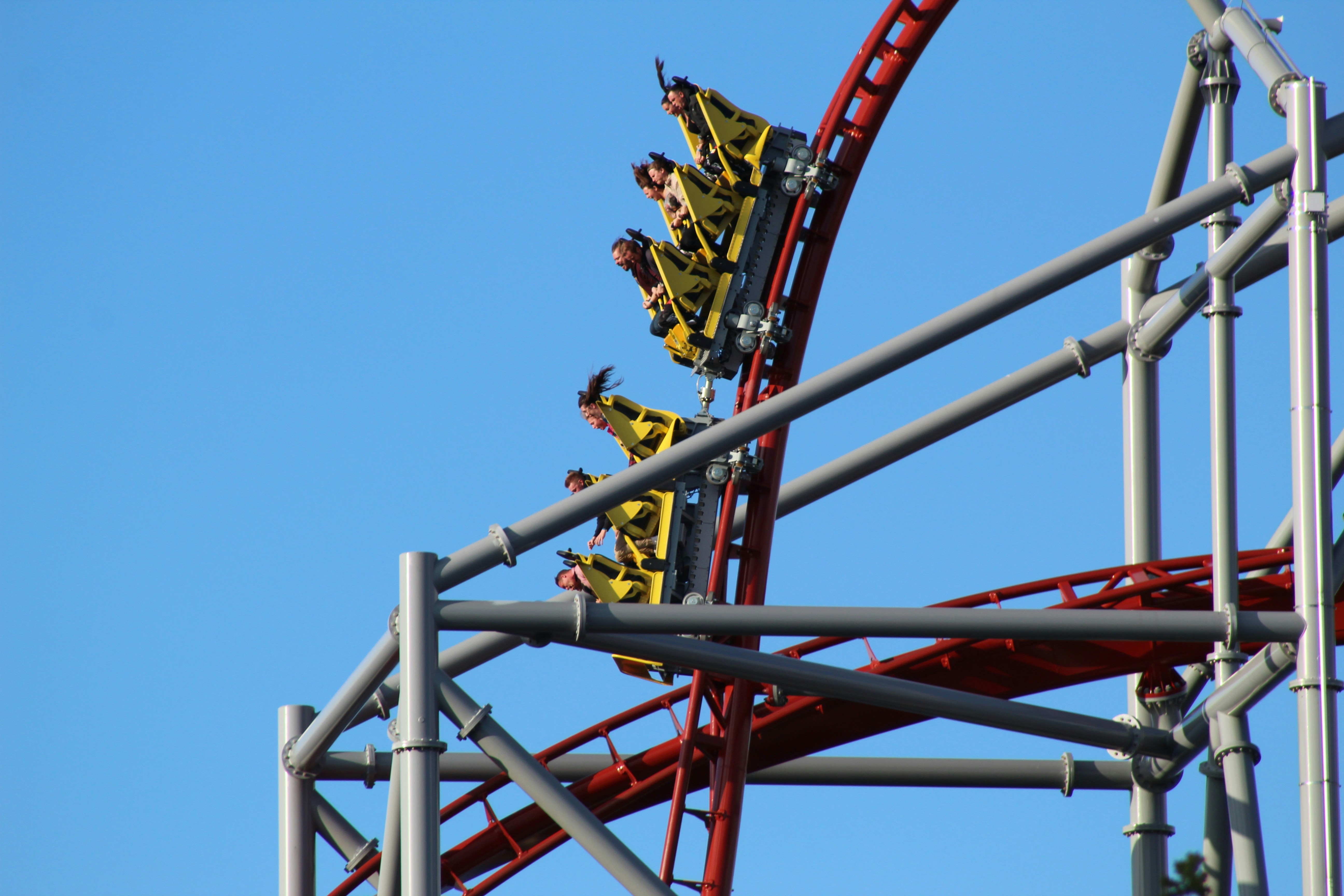 Riders in Yellow Abreast a Crimson Roller Coaster Against a Bright Sky