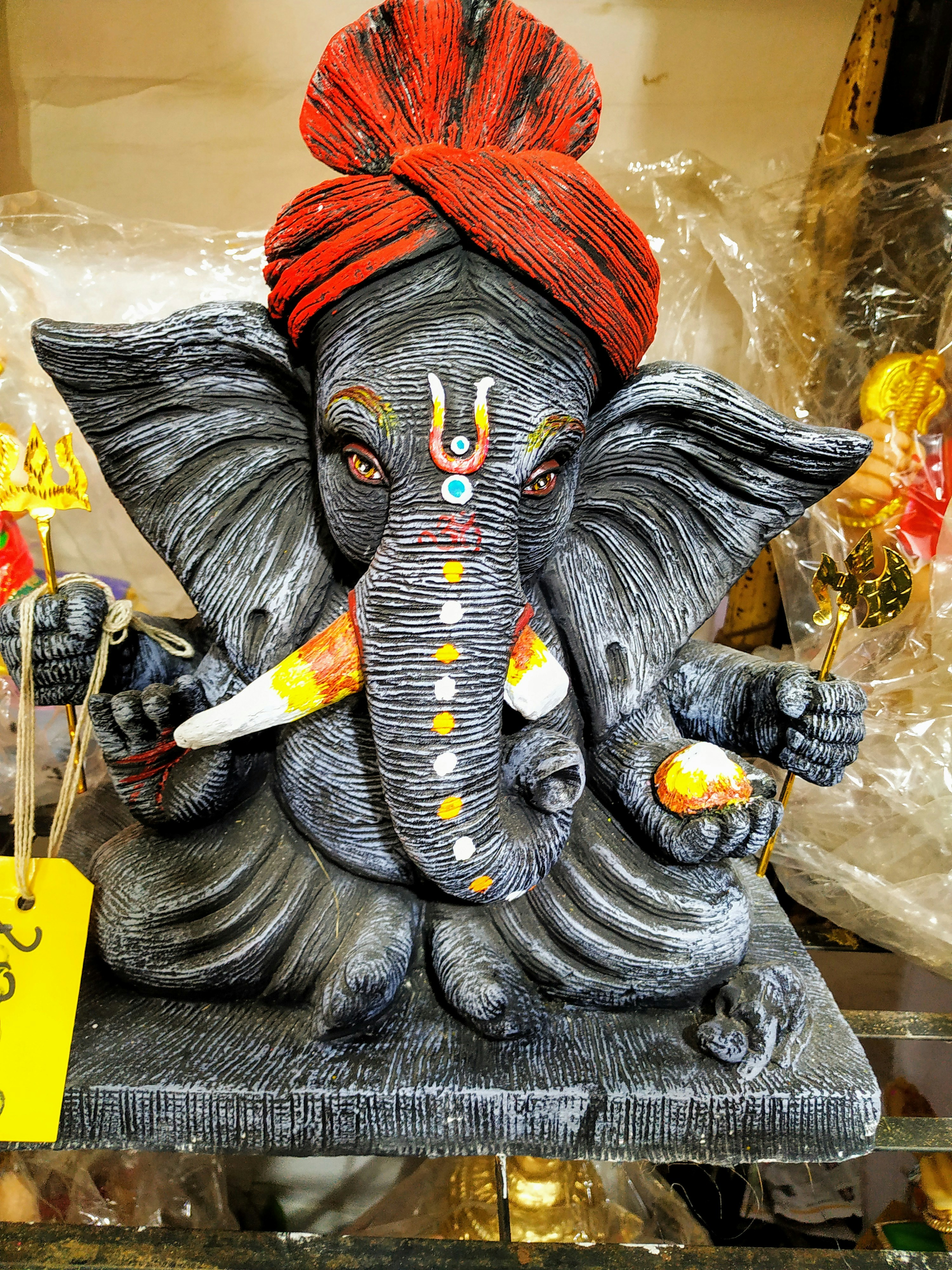 Ganesha statue with orange turban and painted trunk sits amid market glow