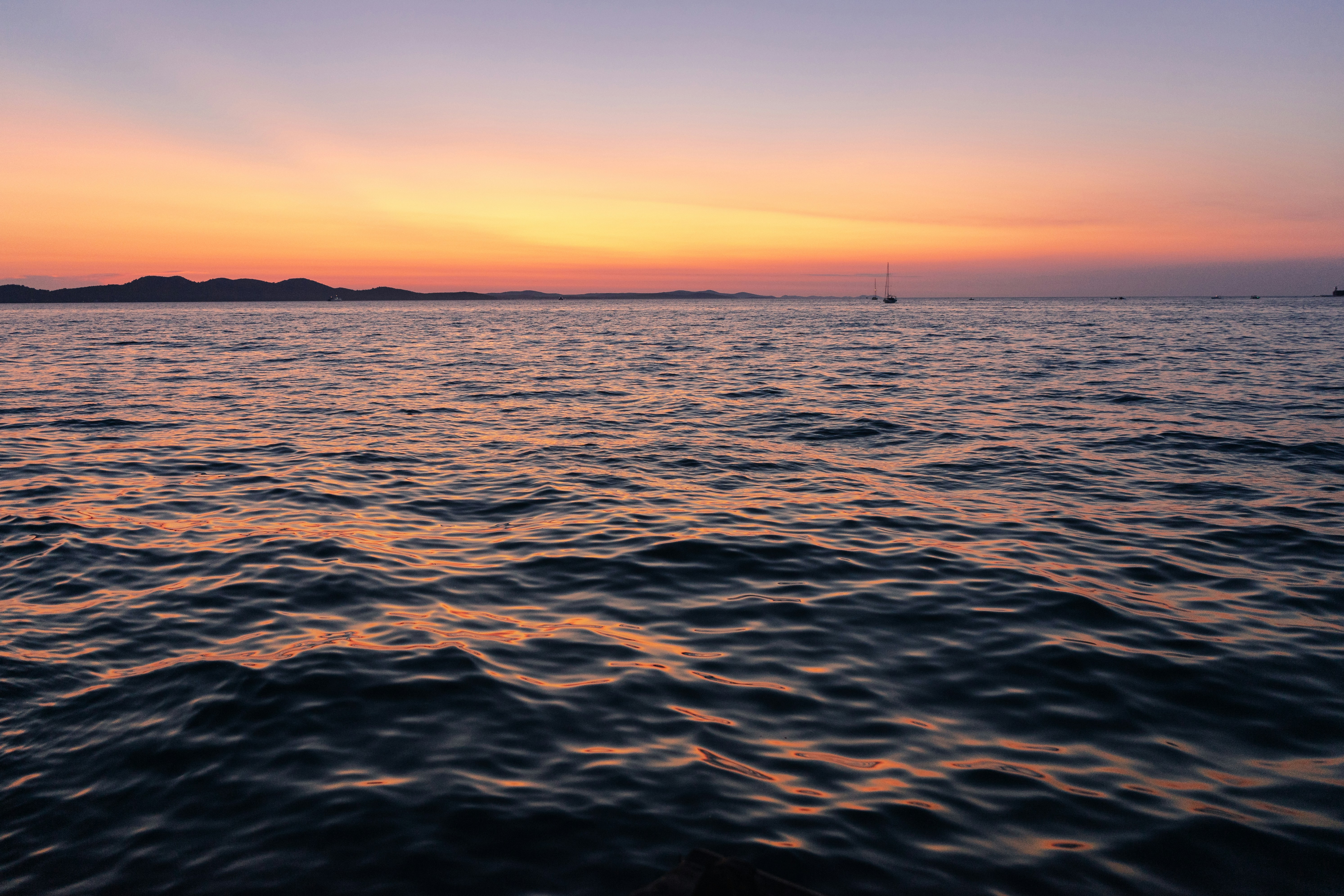 Sunset over a calm sea with gentle waves under a colorful sky.