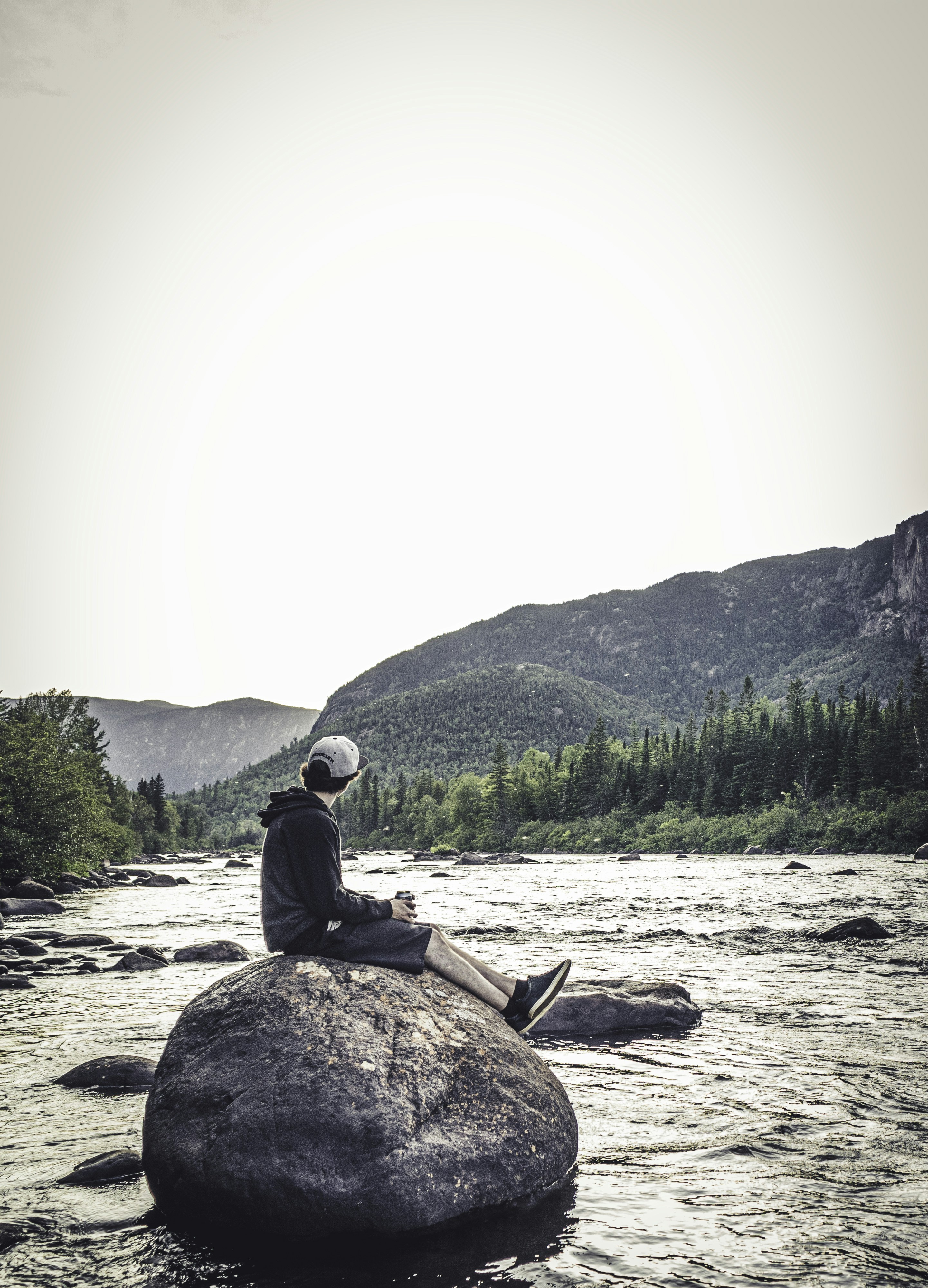 Man sitting on rock viewing river and mountain during daytime photo ...