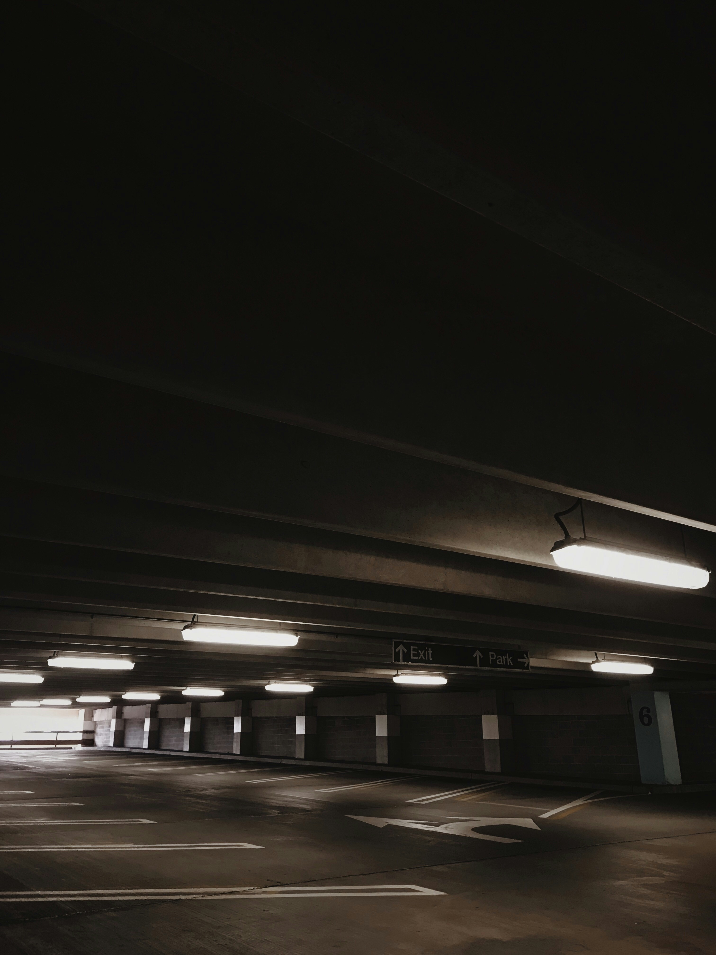 Dimly lit parking garage featuring overhead lights and directional signs. A sense of solitude permeates the space.